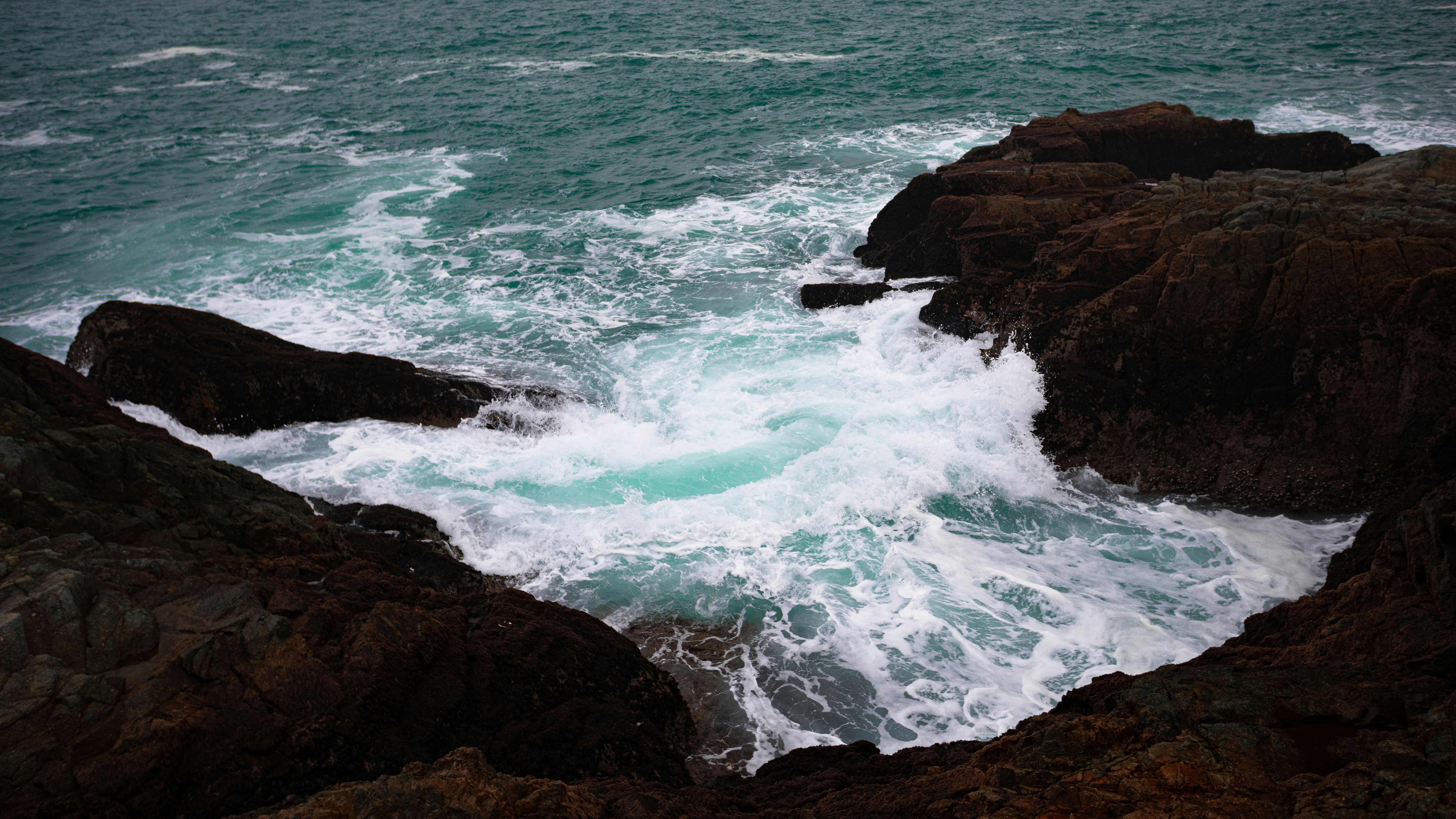 Foamy waves crashing against rugged rocks along a coastal shoreline, capturing the raw energy of nature.