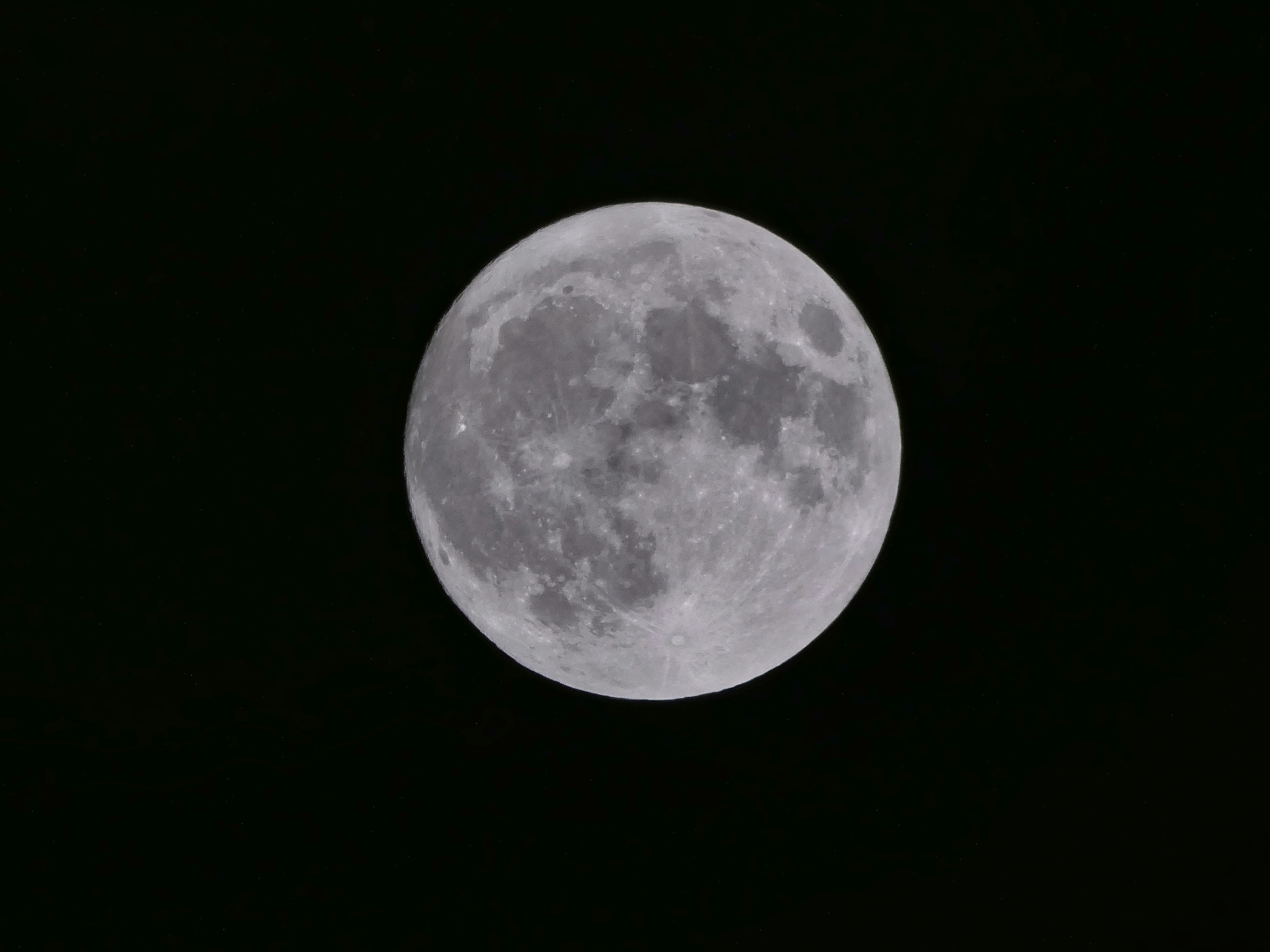Full moon illuminated against a stark black sky, showcasing its craters and surface details.