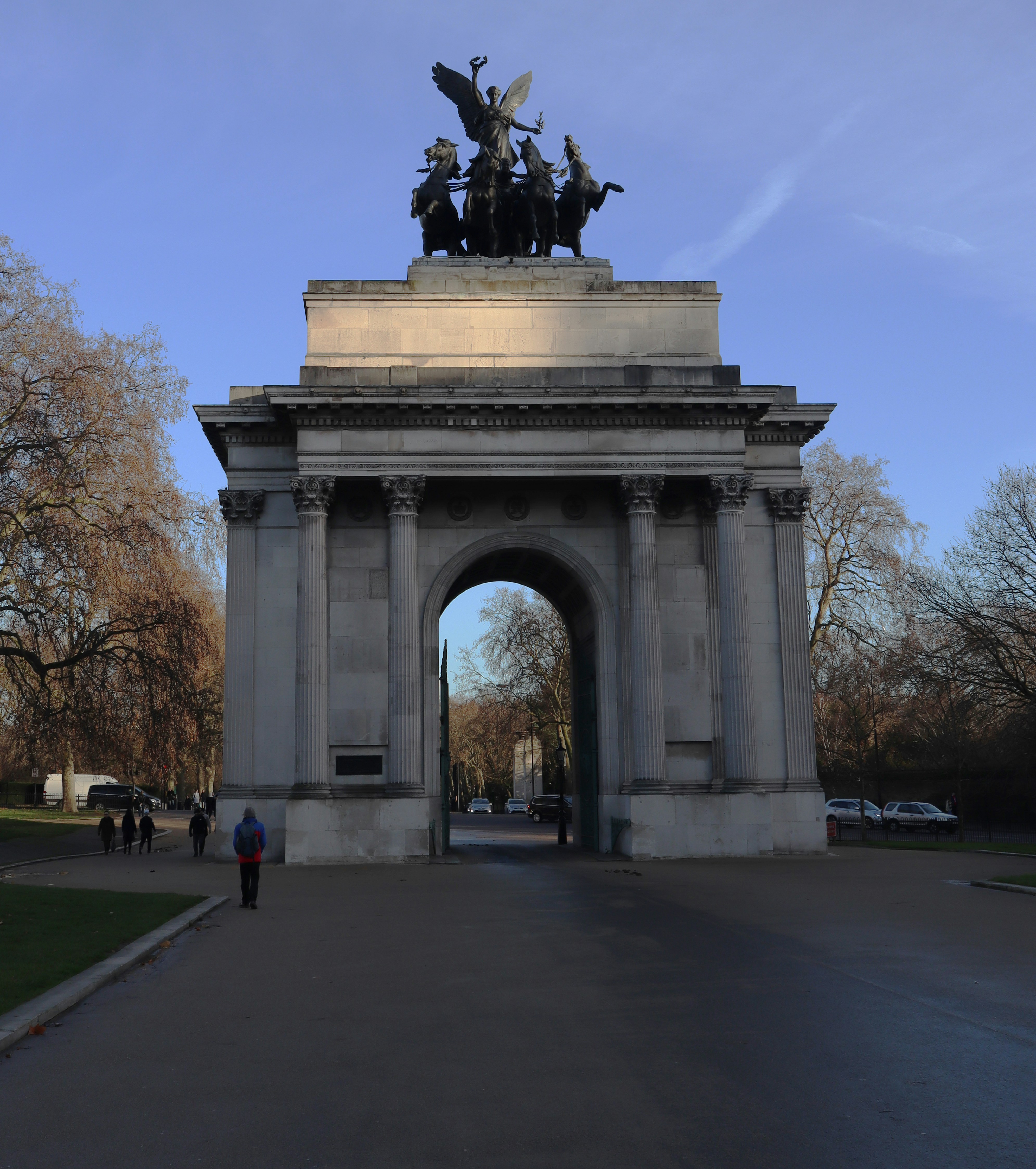 Wellington Arch framed by bare trees under a clear blue sky.