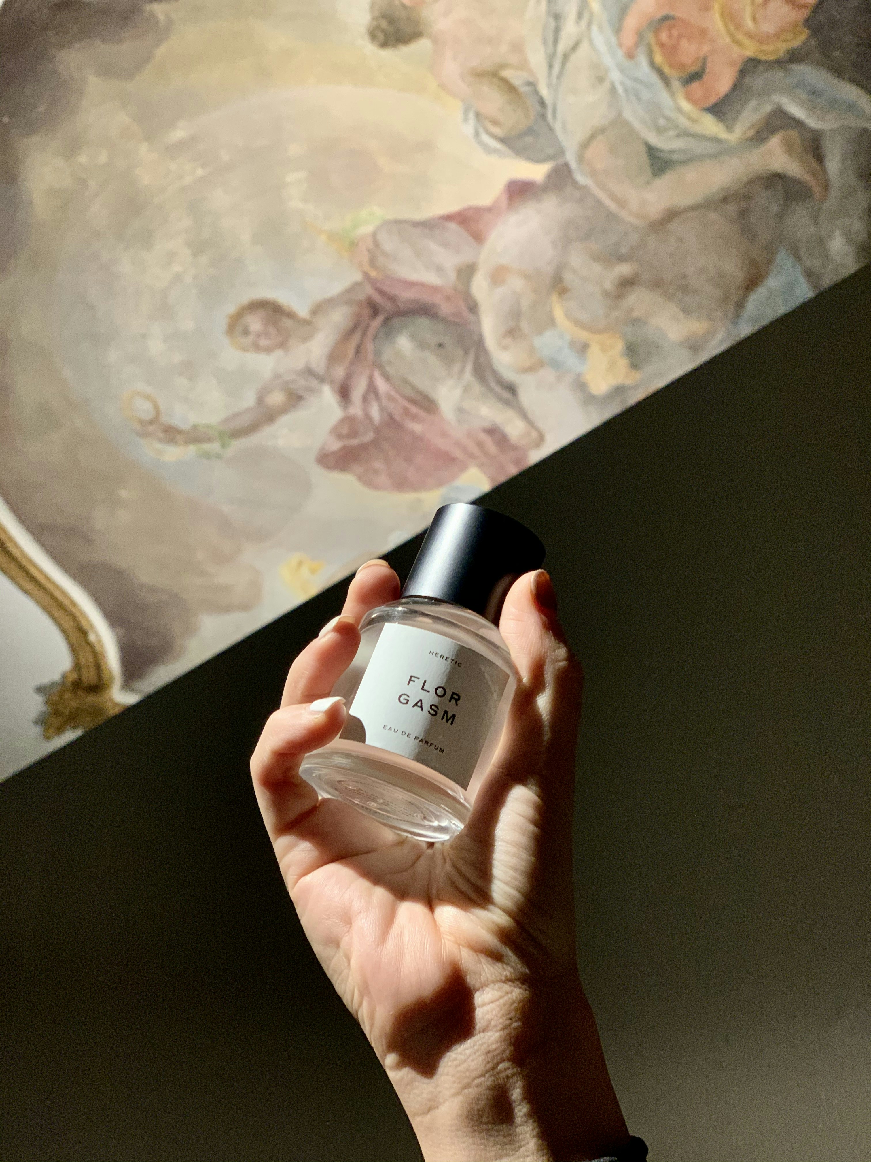 Petite perfume in hand against diagonal art backdrop