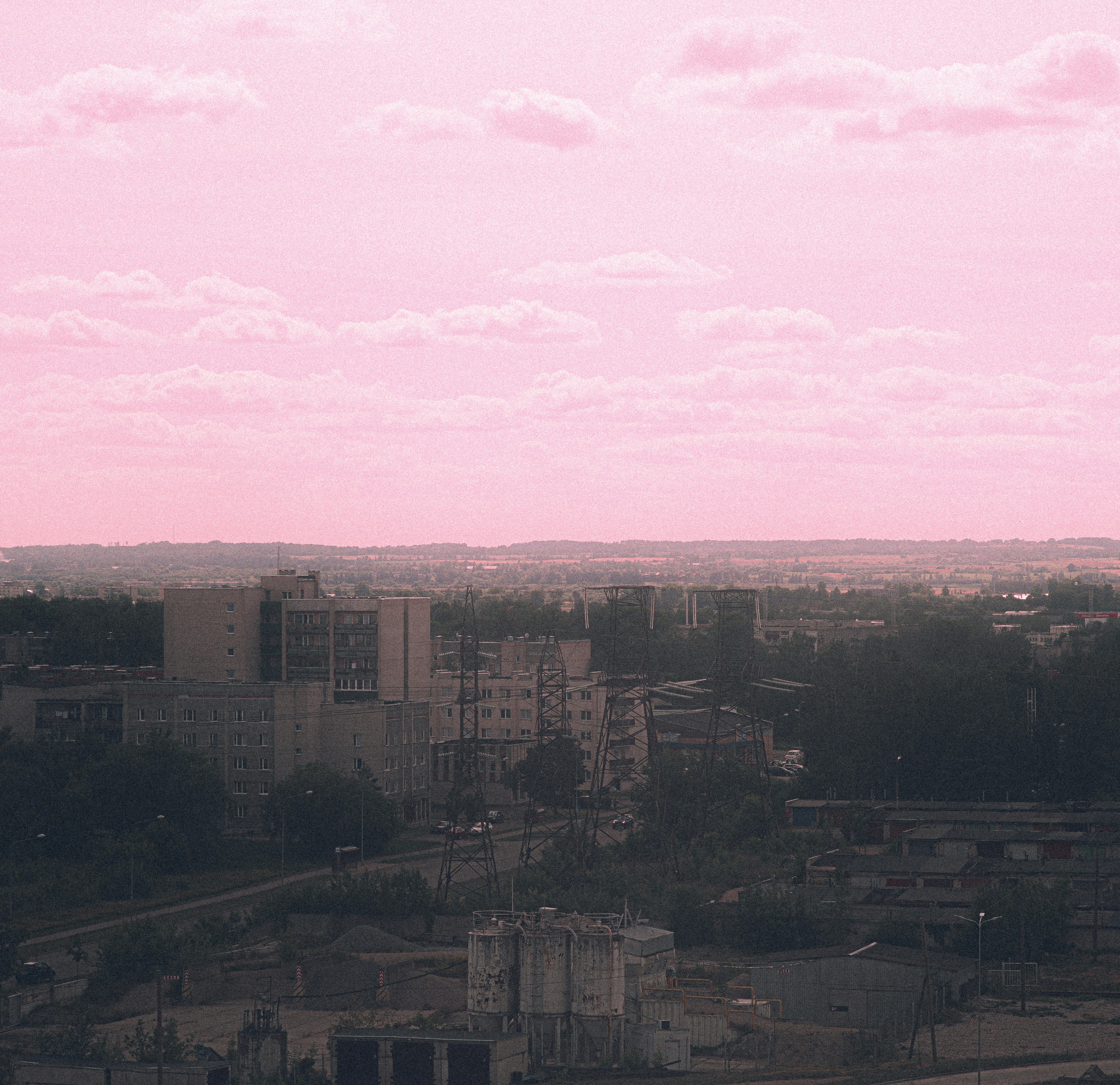 A panoramic view of a cityscape beneath a pastel pink sky, showcasing a blend of modern buildings and industrial structures.