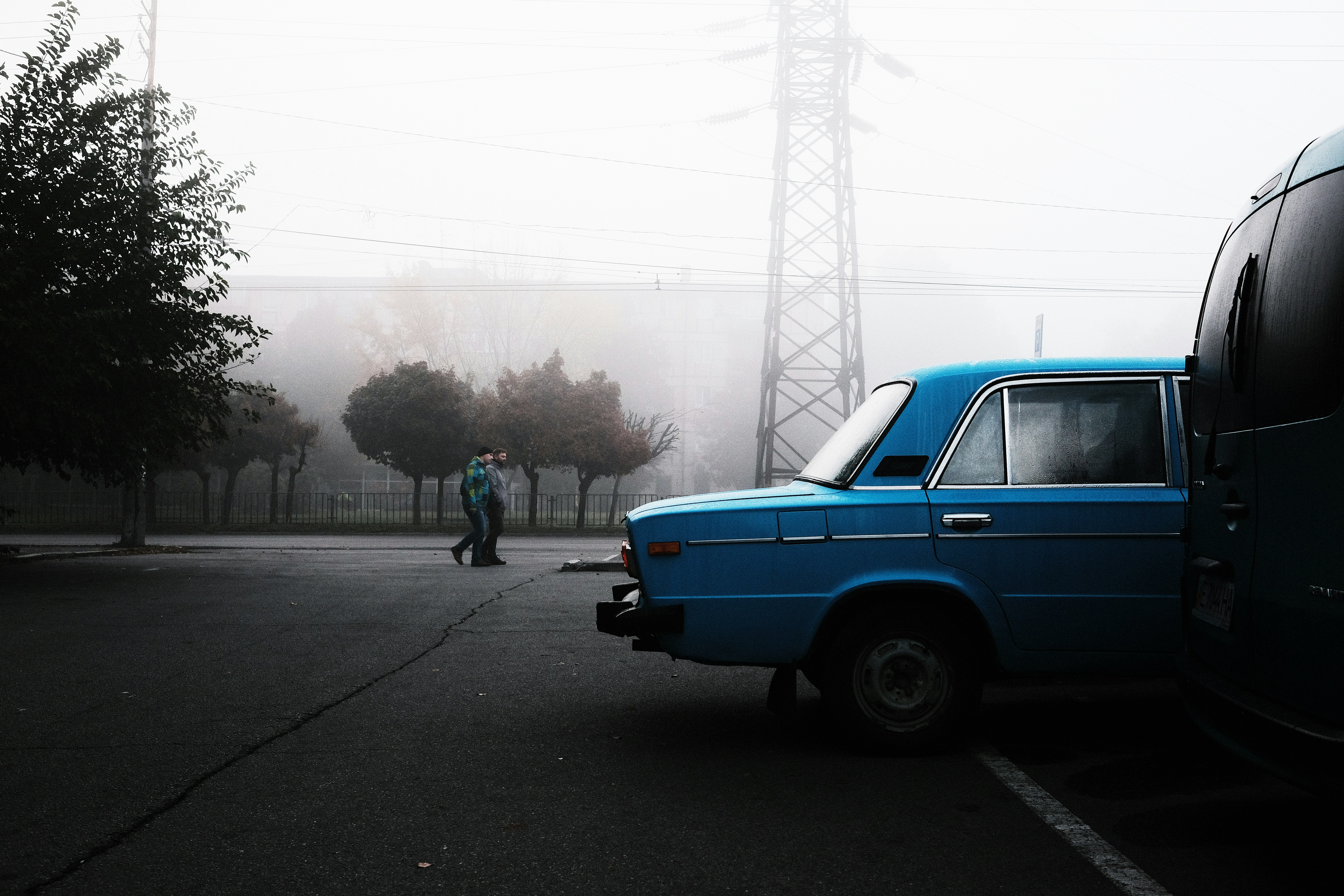 Blue Vintage Sedan in a Fog-Kissed Parking Lot with a Distant Pedestrian