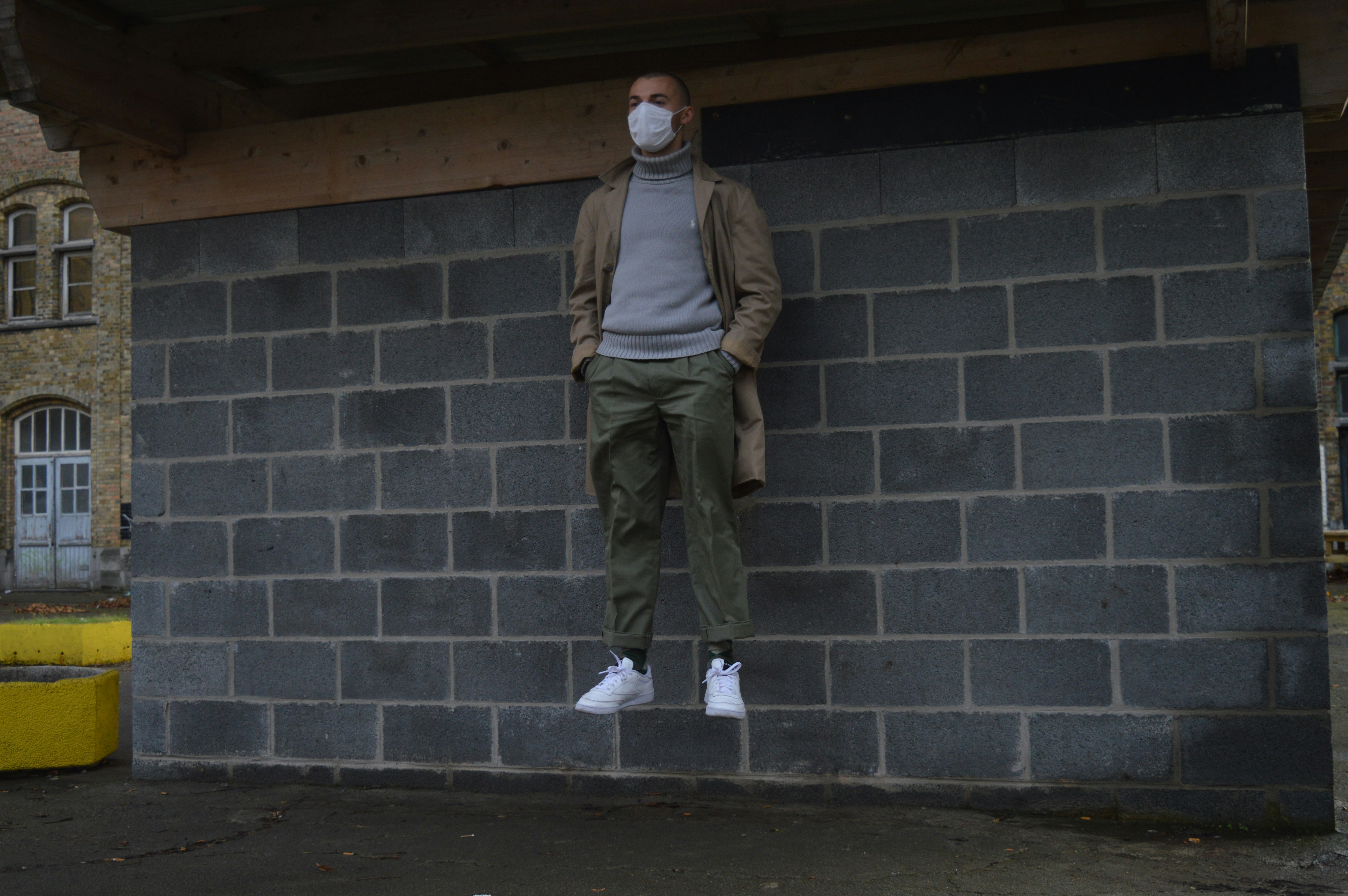 Masked Figure in a Trench Coat Leans Against a Slate Brick Wall