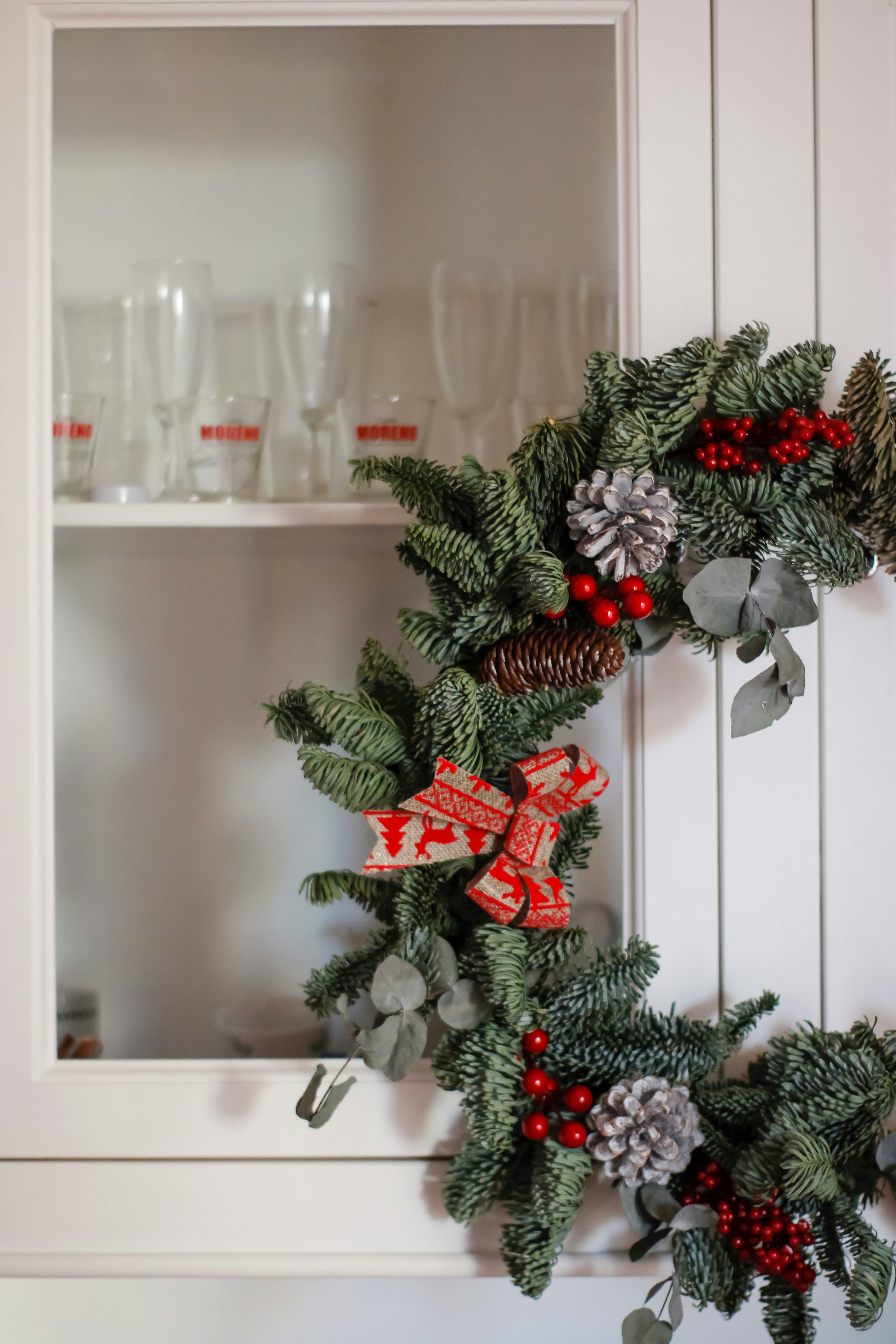 Seasonal wreath drapes a white cabinet with glassware tucked behind a frosted window