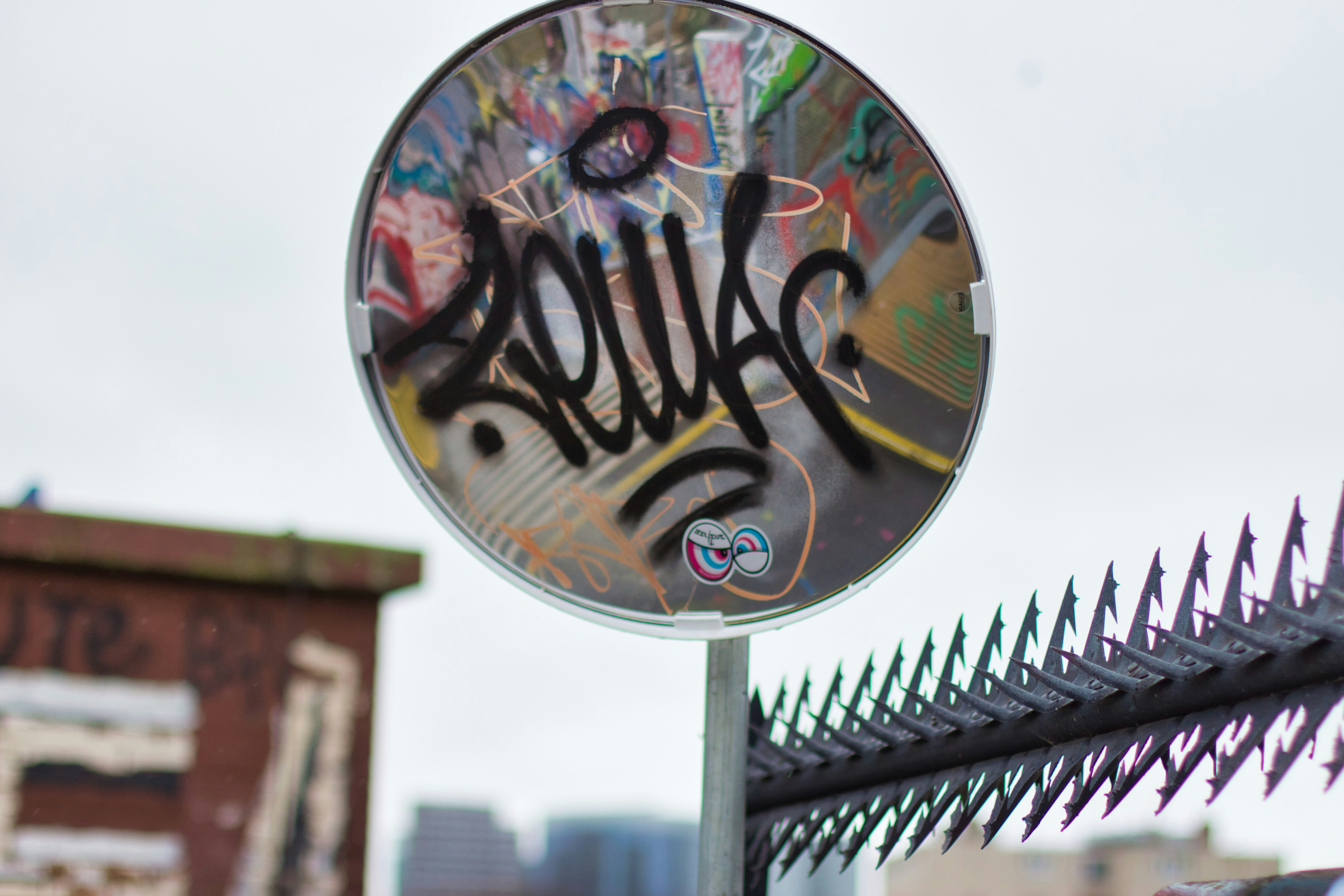 Urban Echo: Graffiti-Splashed Convex Mirror Framed by Barbed Wire