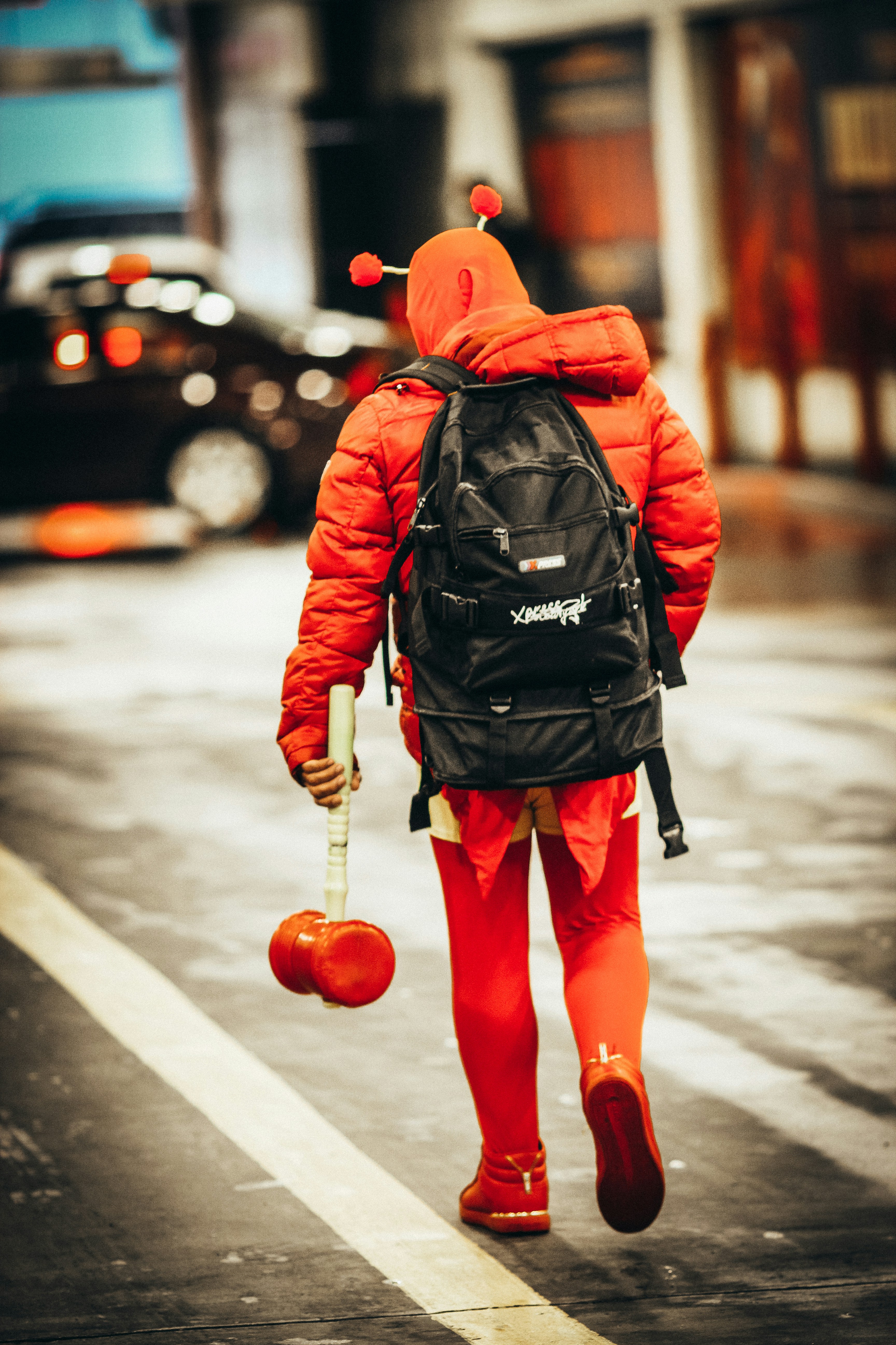 person in orange jacket and black backpack walking on street during daytime