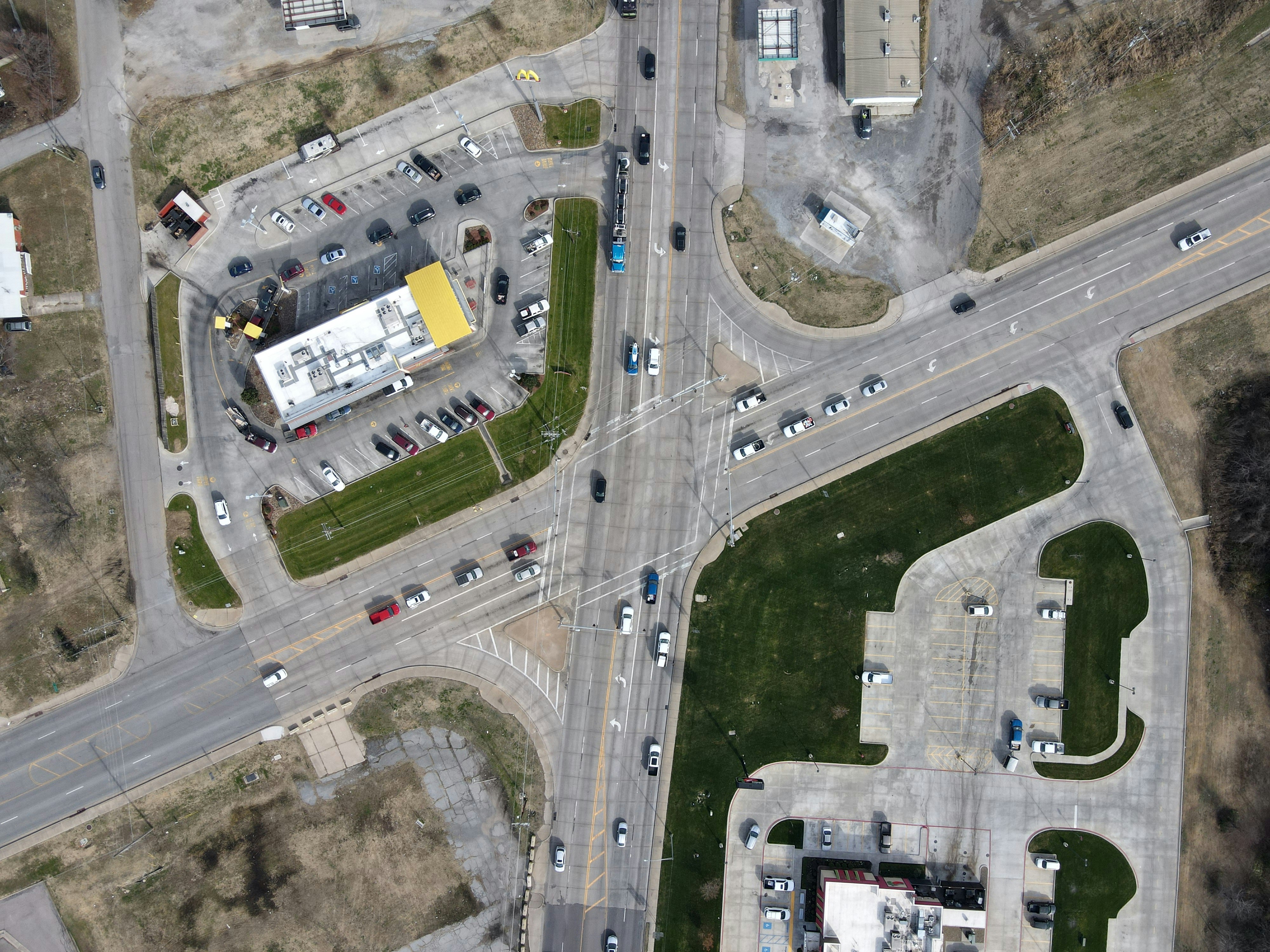 Aerial view of a bustling urban intersection with vehicles navigating multiple roads and a fast-food restaurant at the center.