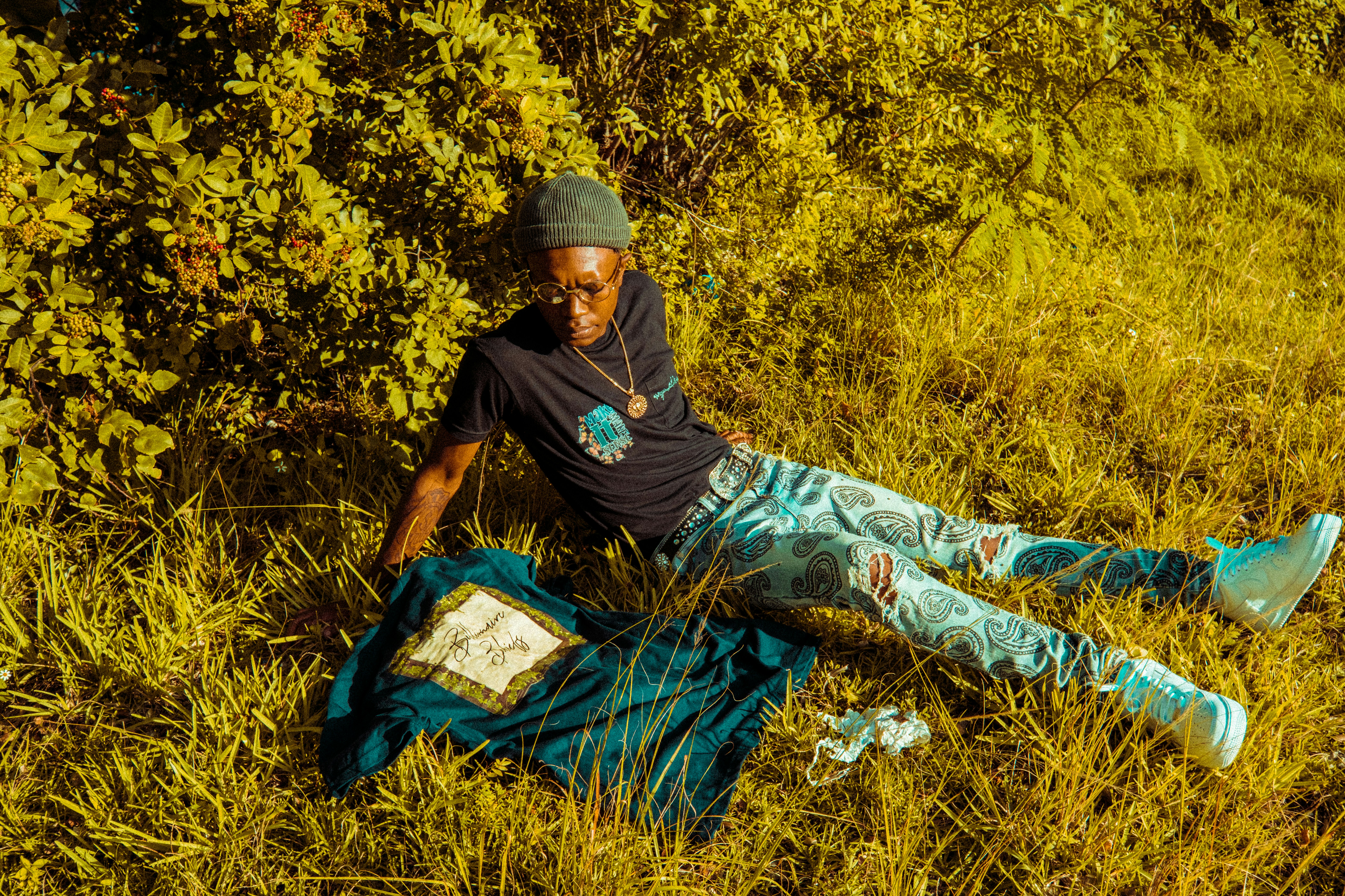 Individual lounging in vibrant clothing on a blanket amidst lush greenery, capturing a serene outdoor vibe.