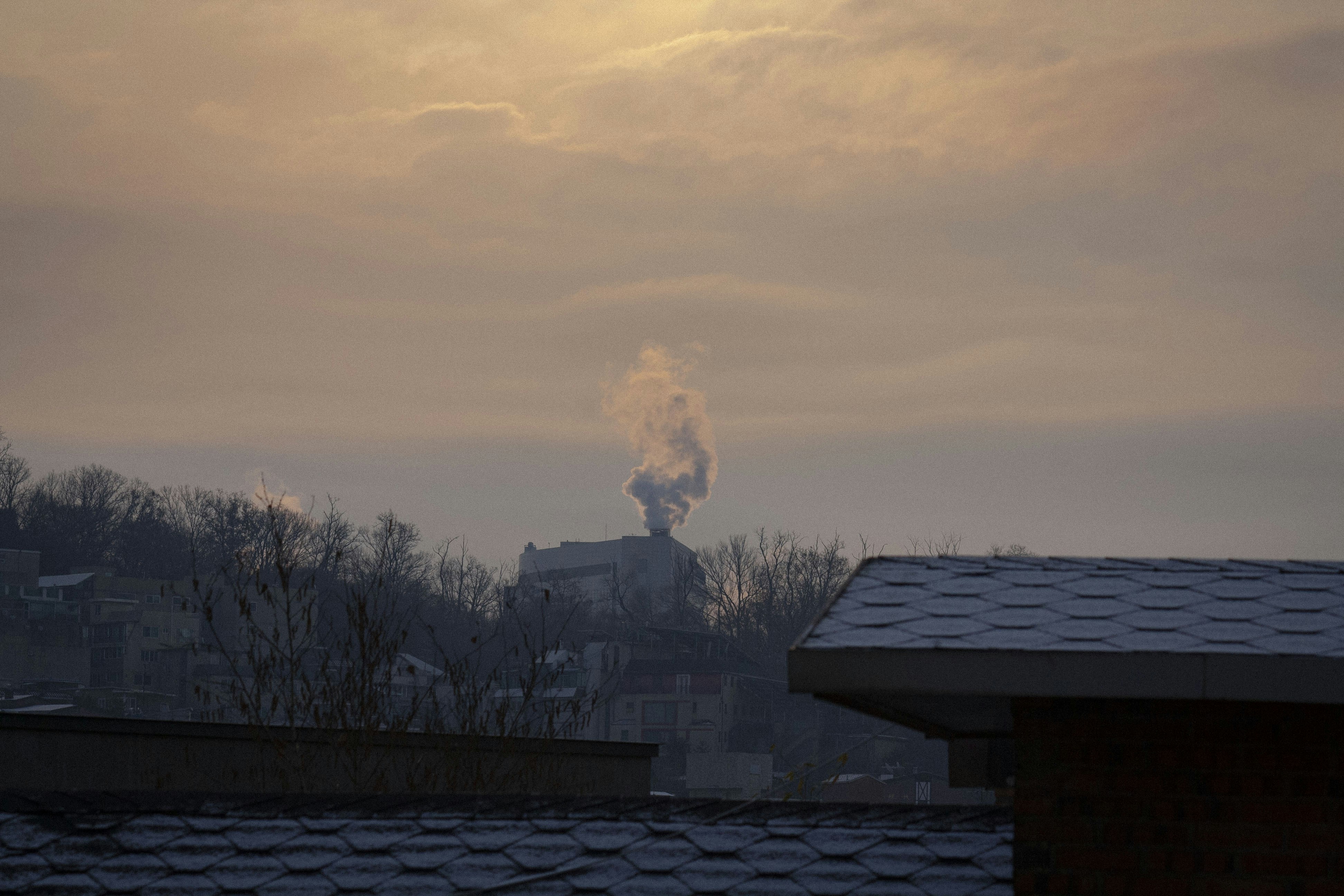 Smokestack in the haze: winter rooftops overlook a distant plume at dusk