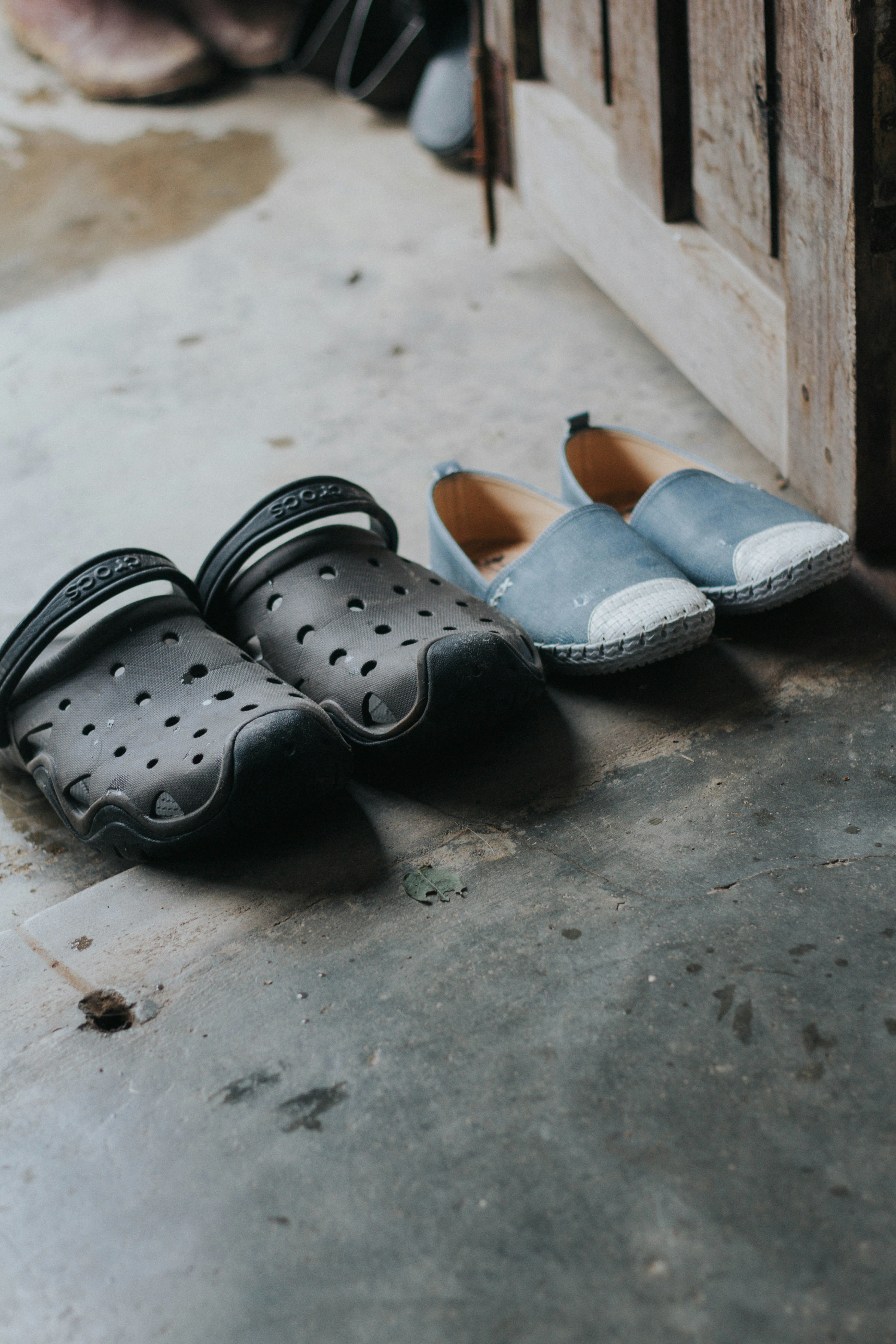 Doorstep Duet: Black Crocs and Blue Slippers Rest at the Threshold