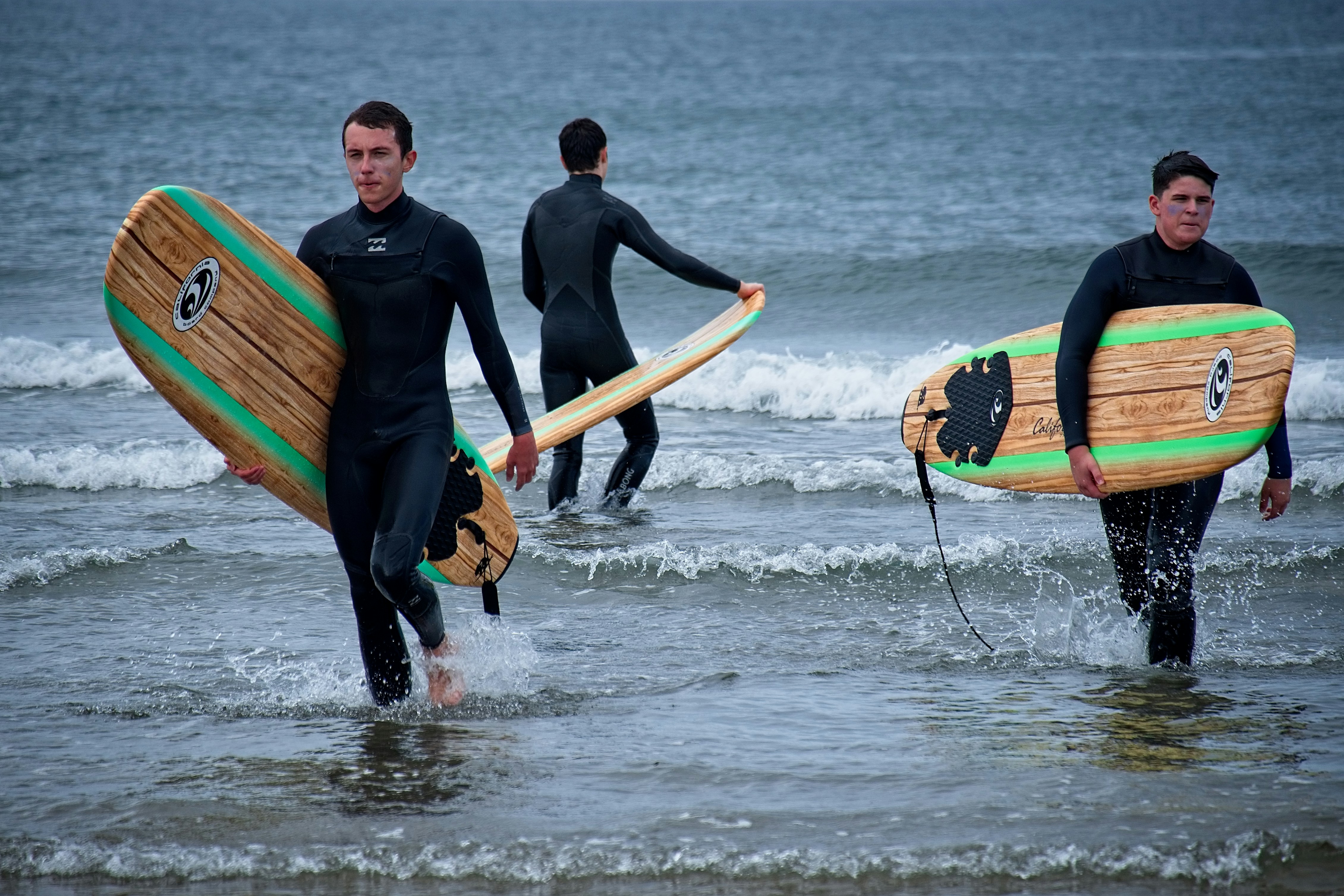 Three Surfers Return from the Tide with their Bright Wooden Boards