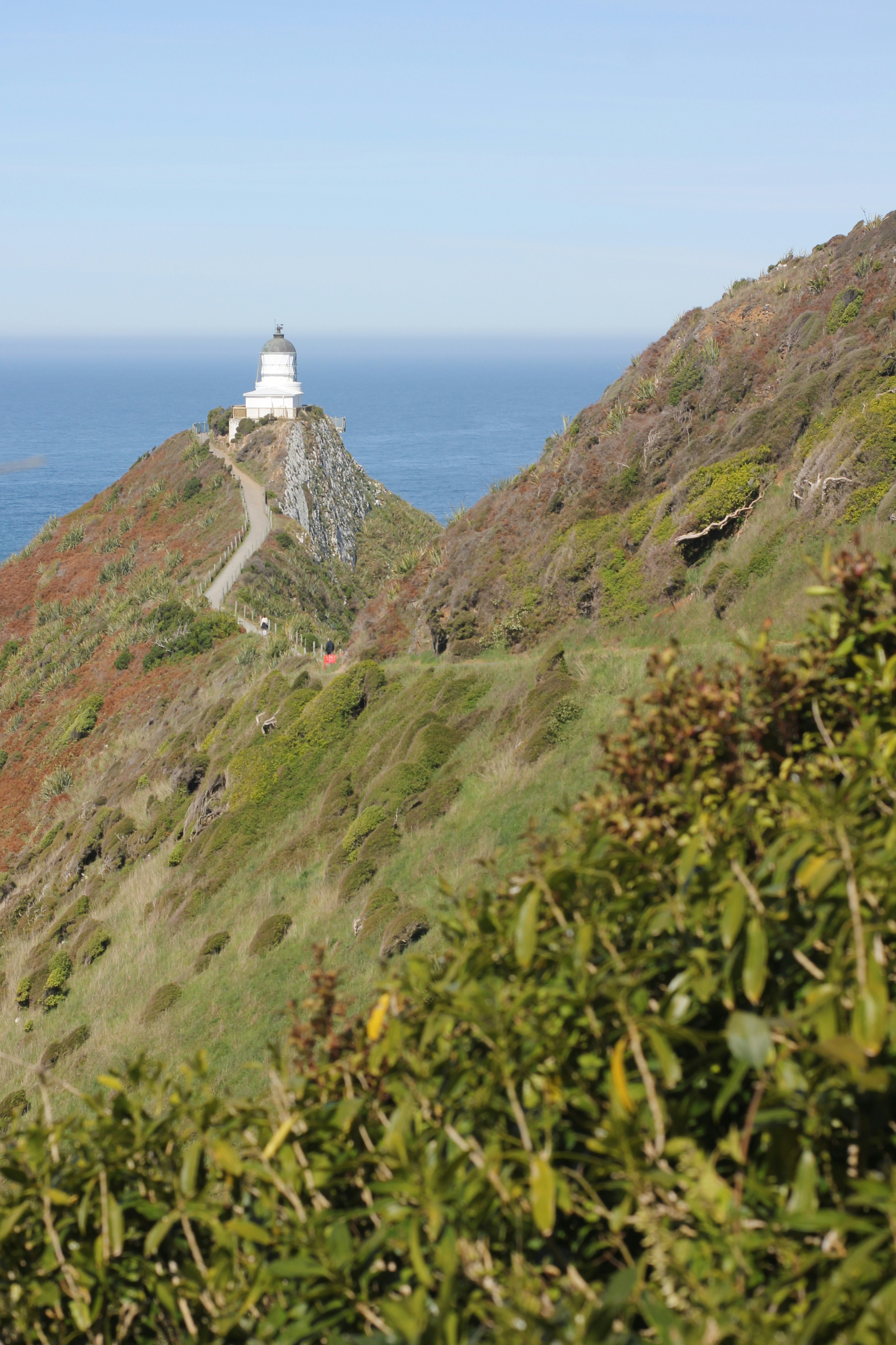 white and black lighthouse on green mountain near body of water during daytime