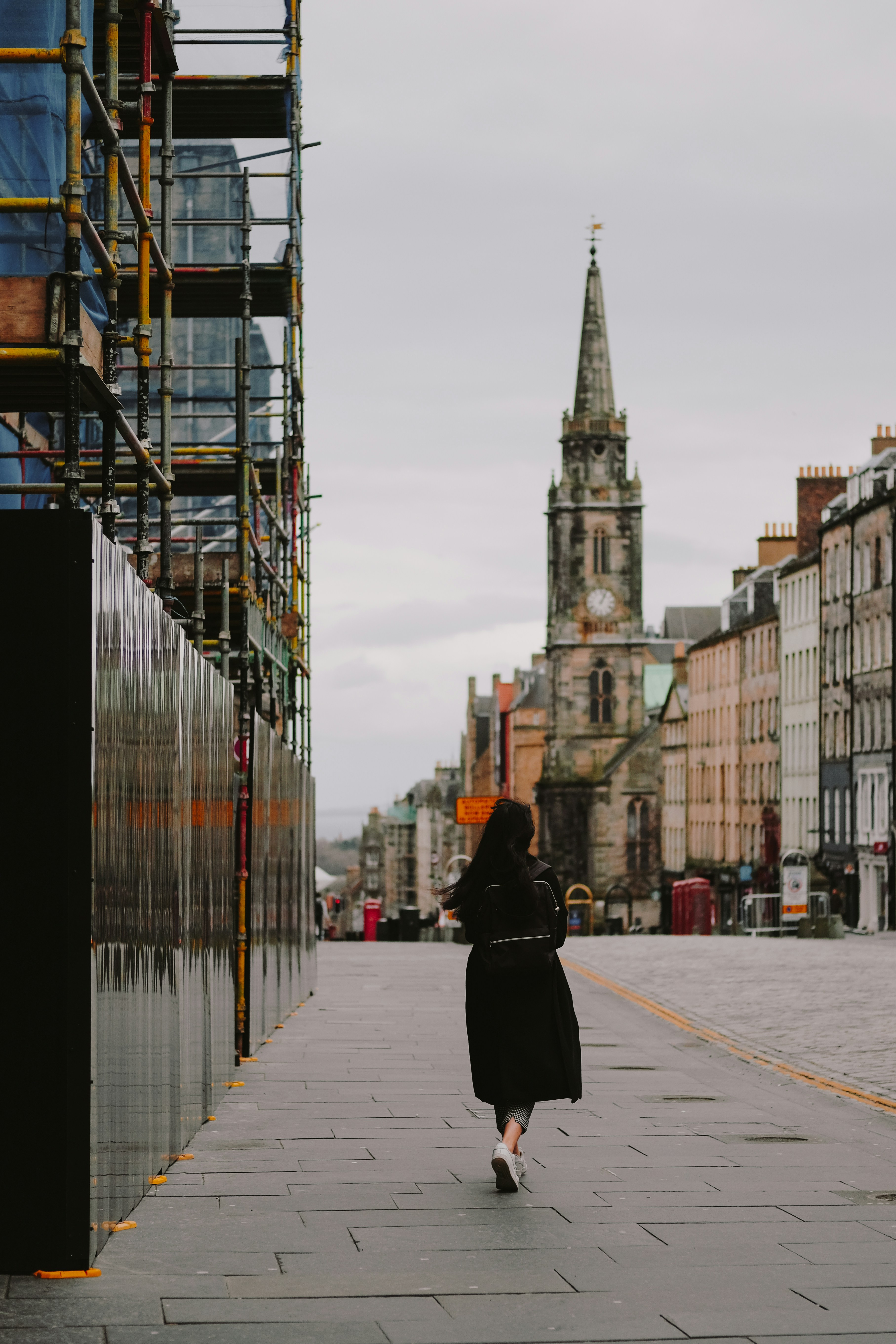 Woman with Coat Walks Toward a Historic Clock Tower on a City Street
