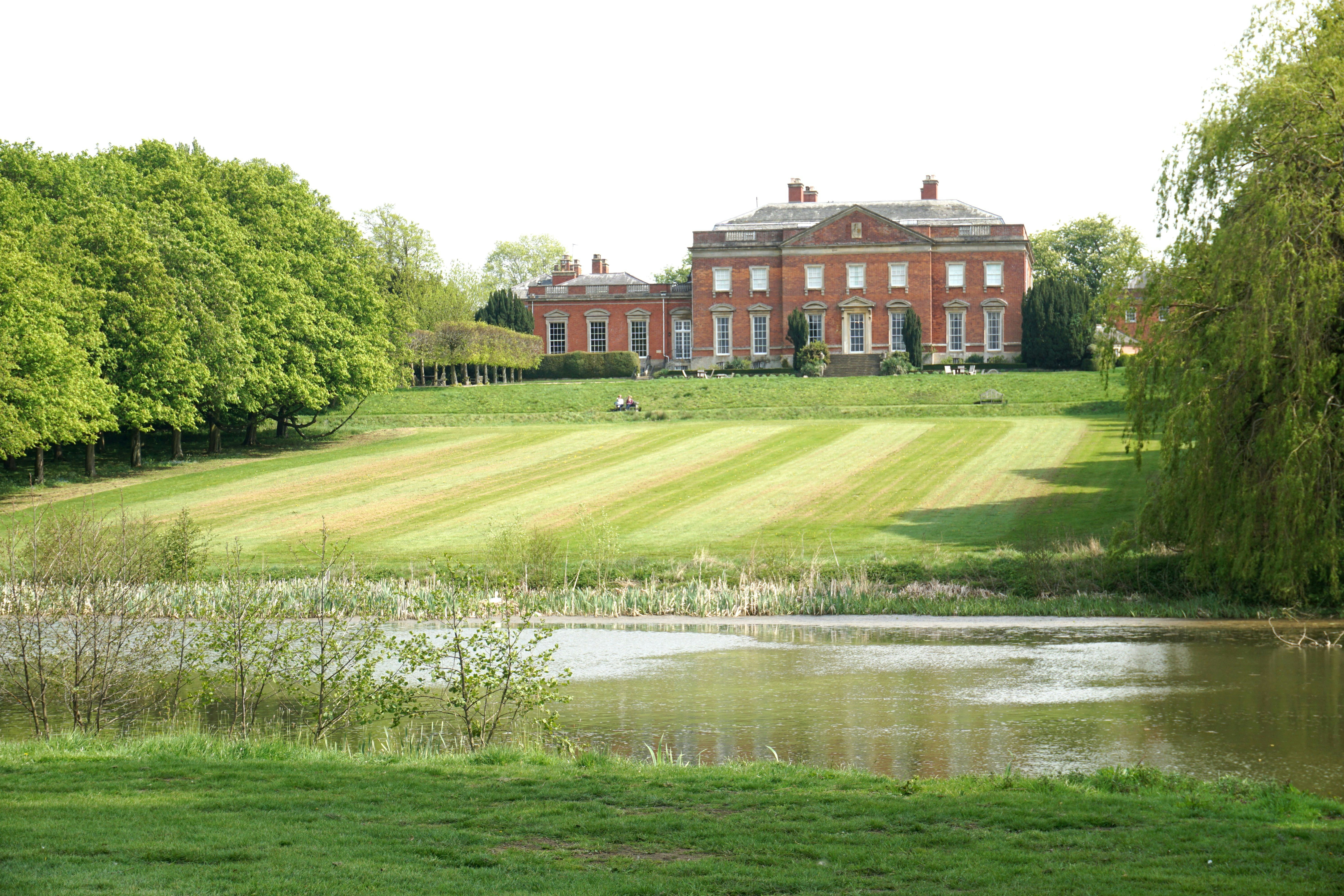 Historic brick mansion overlooking manicured lawns and a reflective pond, framed by lush greenery.