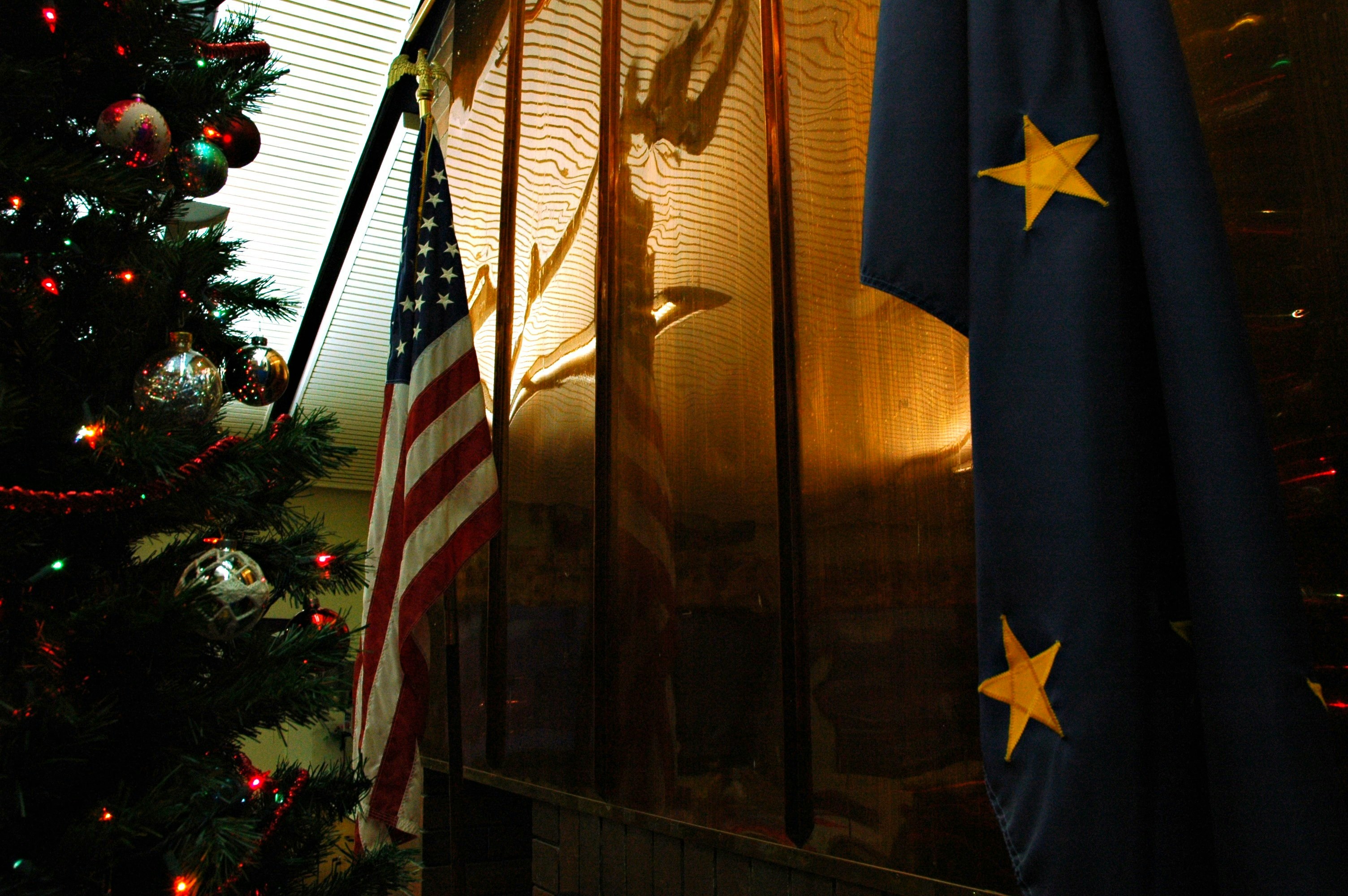 An elegant display featuring an American flag, an Alaskan flag, and a Christmas tree adorned with ornaments, reflecting a warm holiday atmosphere.