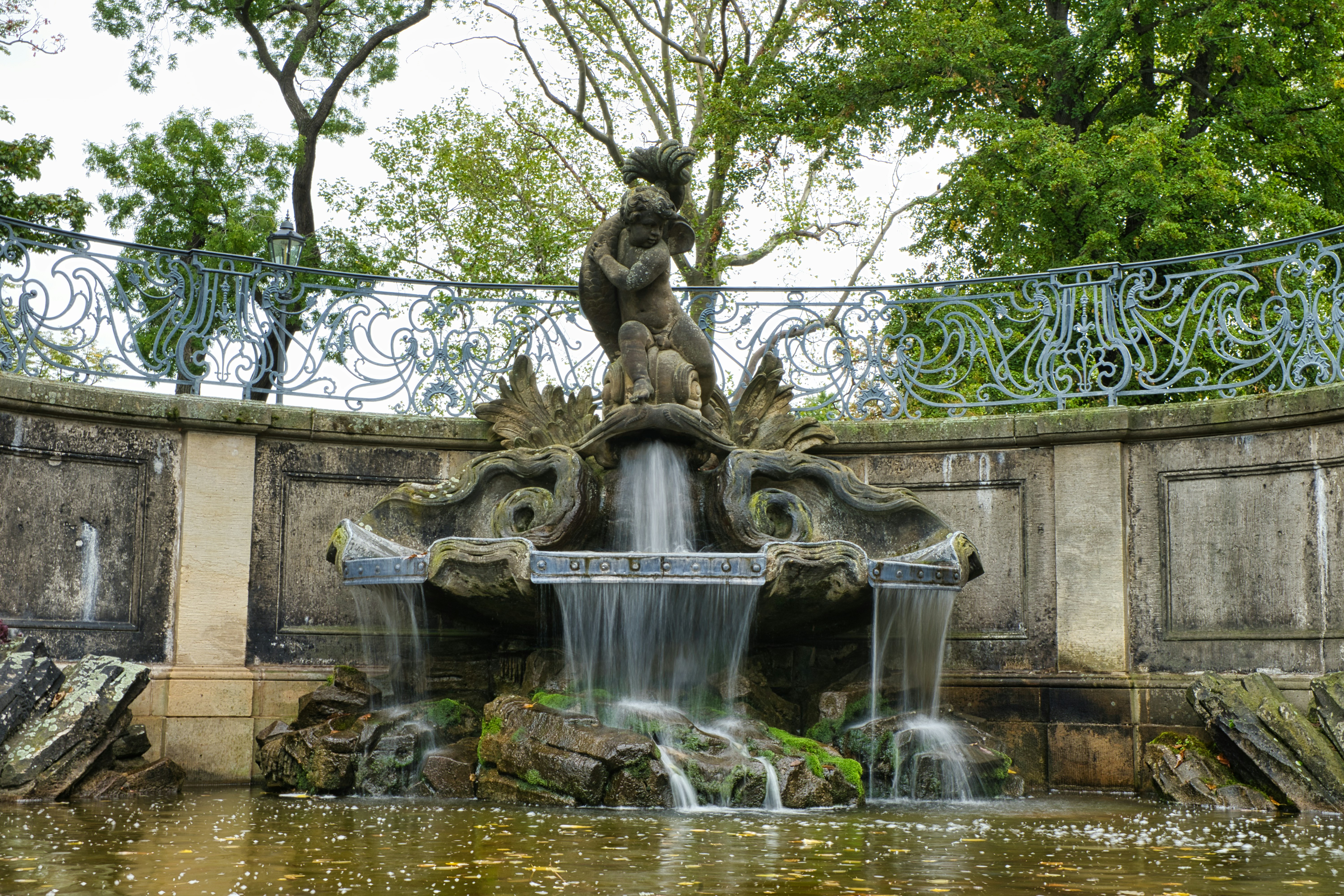 Intricate stone fountain featuring a mythical figure surrounded by flowing water and lush greenery.