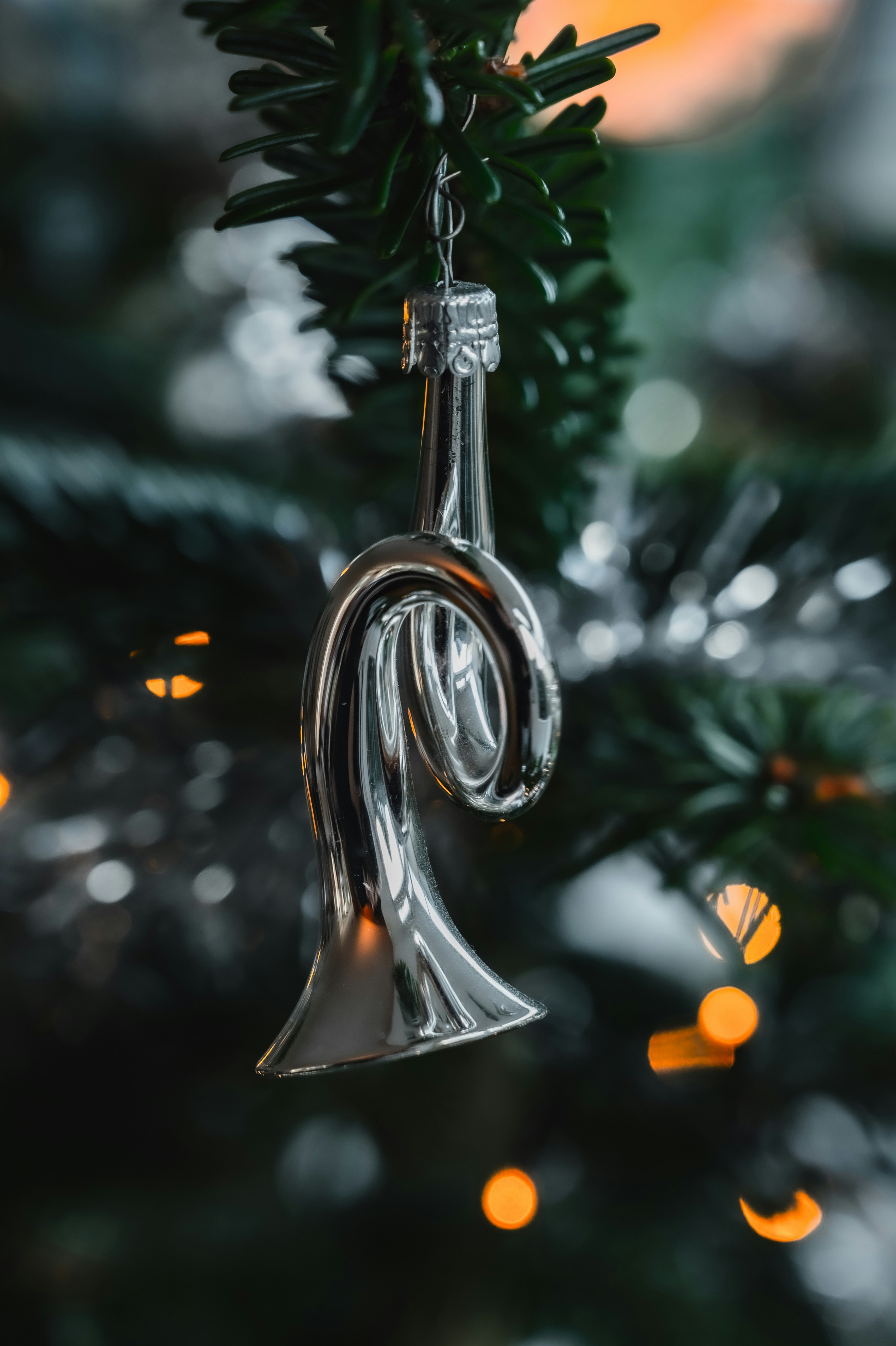 Chrome Horn Ornament Suspended on a Fir Branch, Framed by Warm Holiday Bokeh
