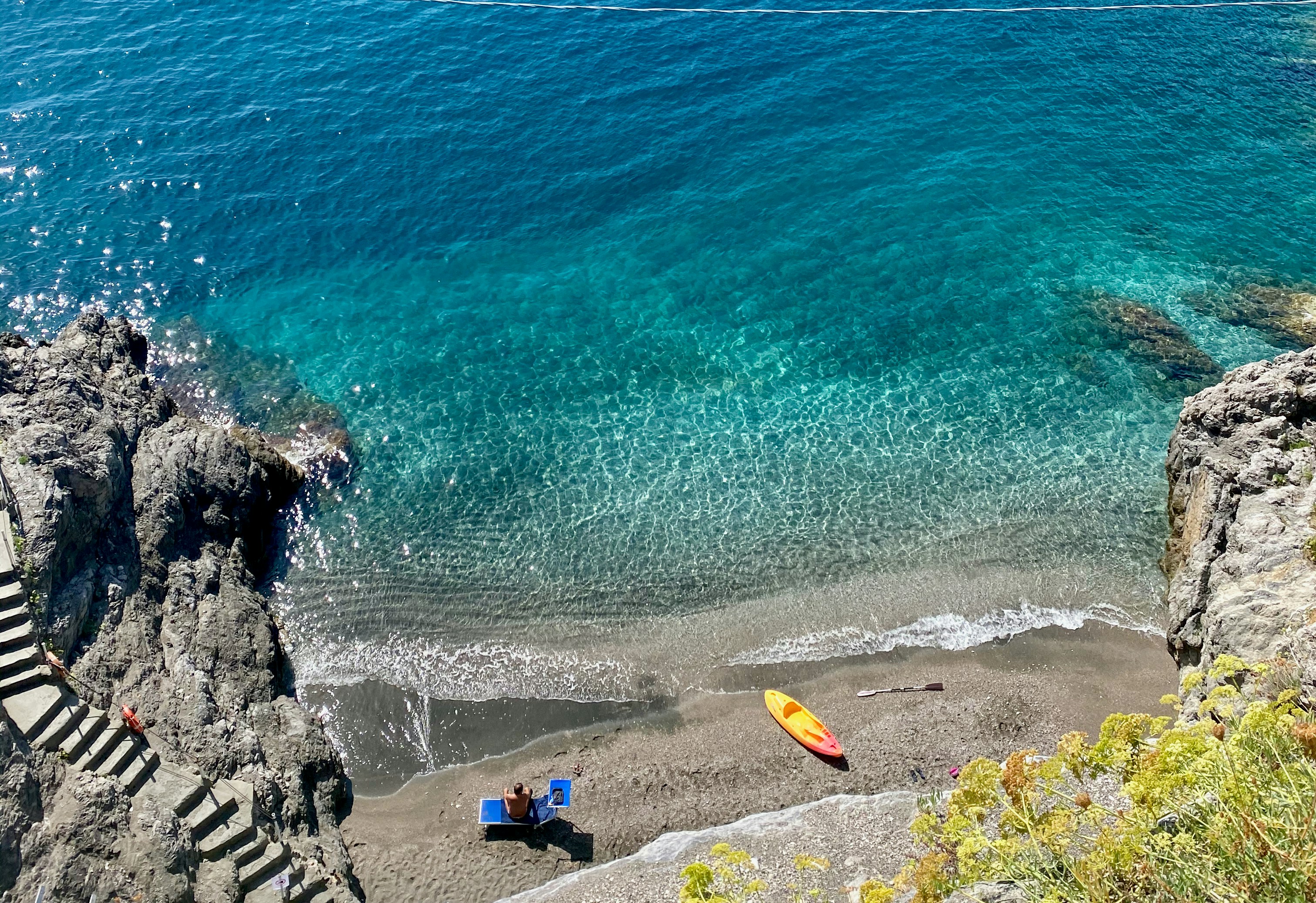 Kayak and beach gear on a secluded rocky shore by clear turquoise waters.