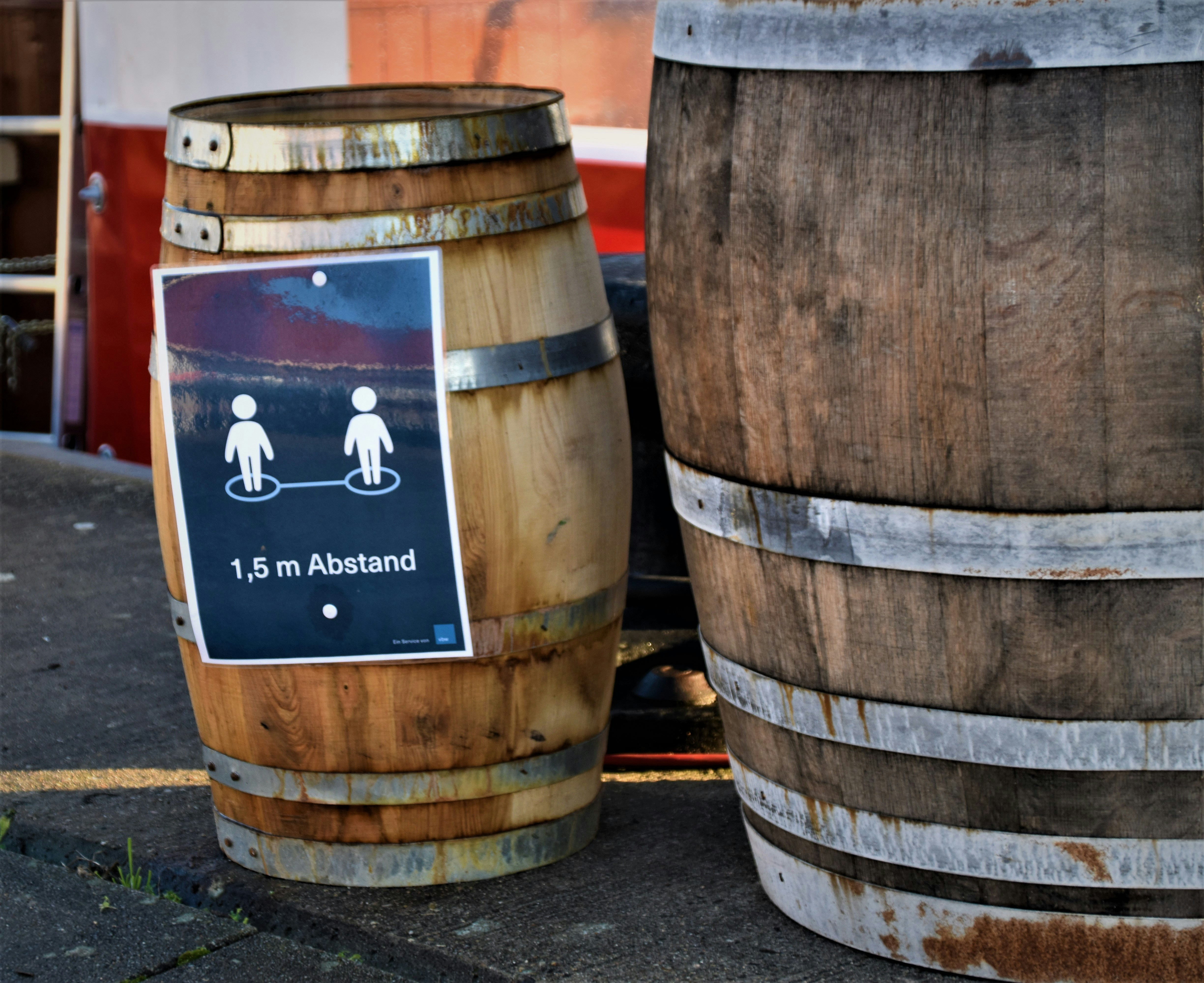 Wooden barrels with a sign indicating a social distancing guideline, emphasizing safety in a casual setting.