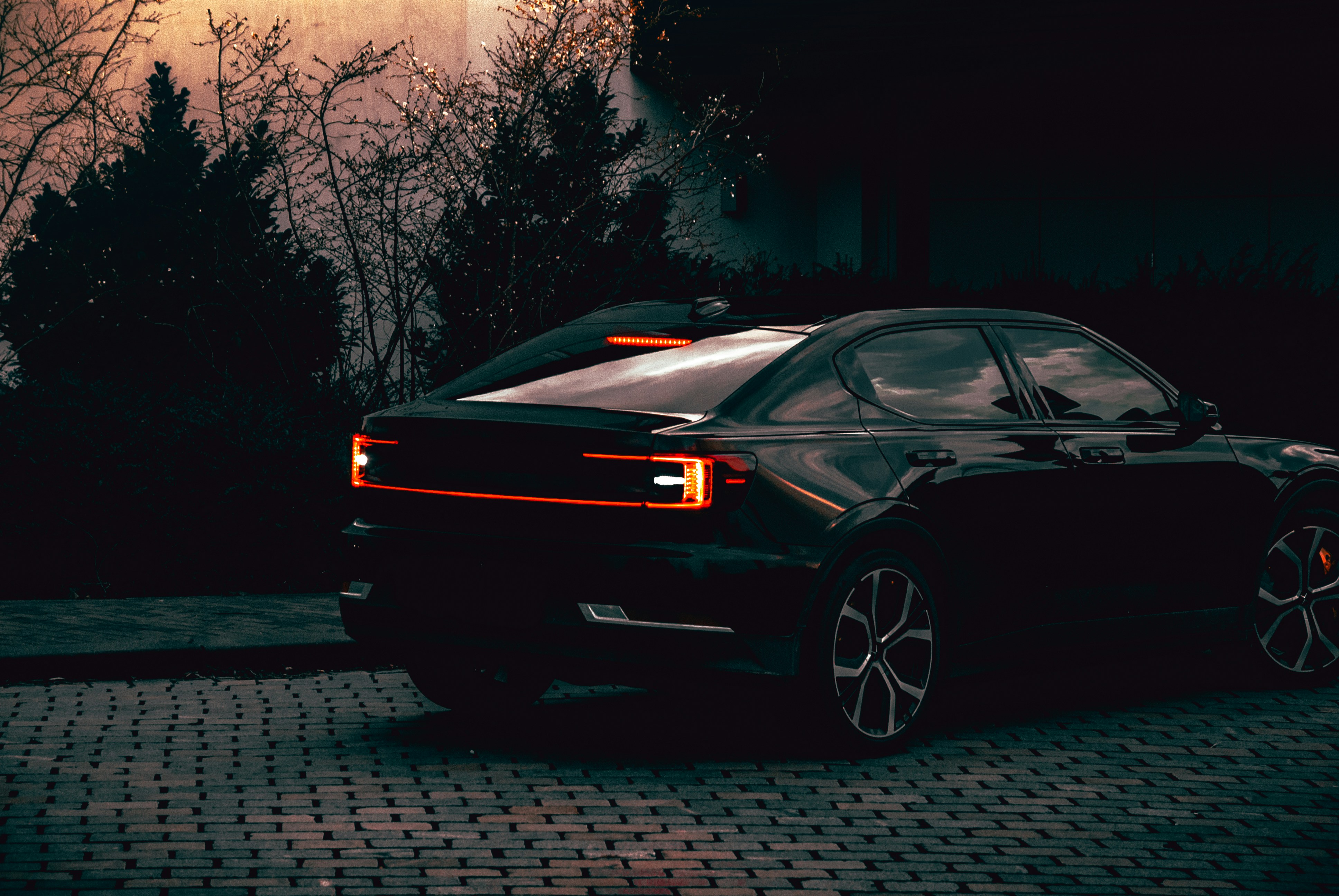 Sleek black car parked under urban lights, showcasing its modern design and illuminated rear lights against a dark backdrop.