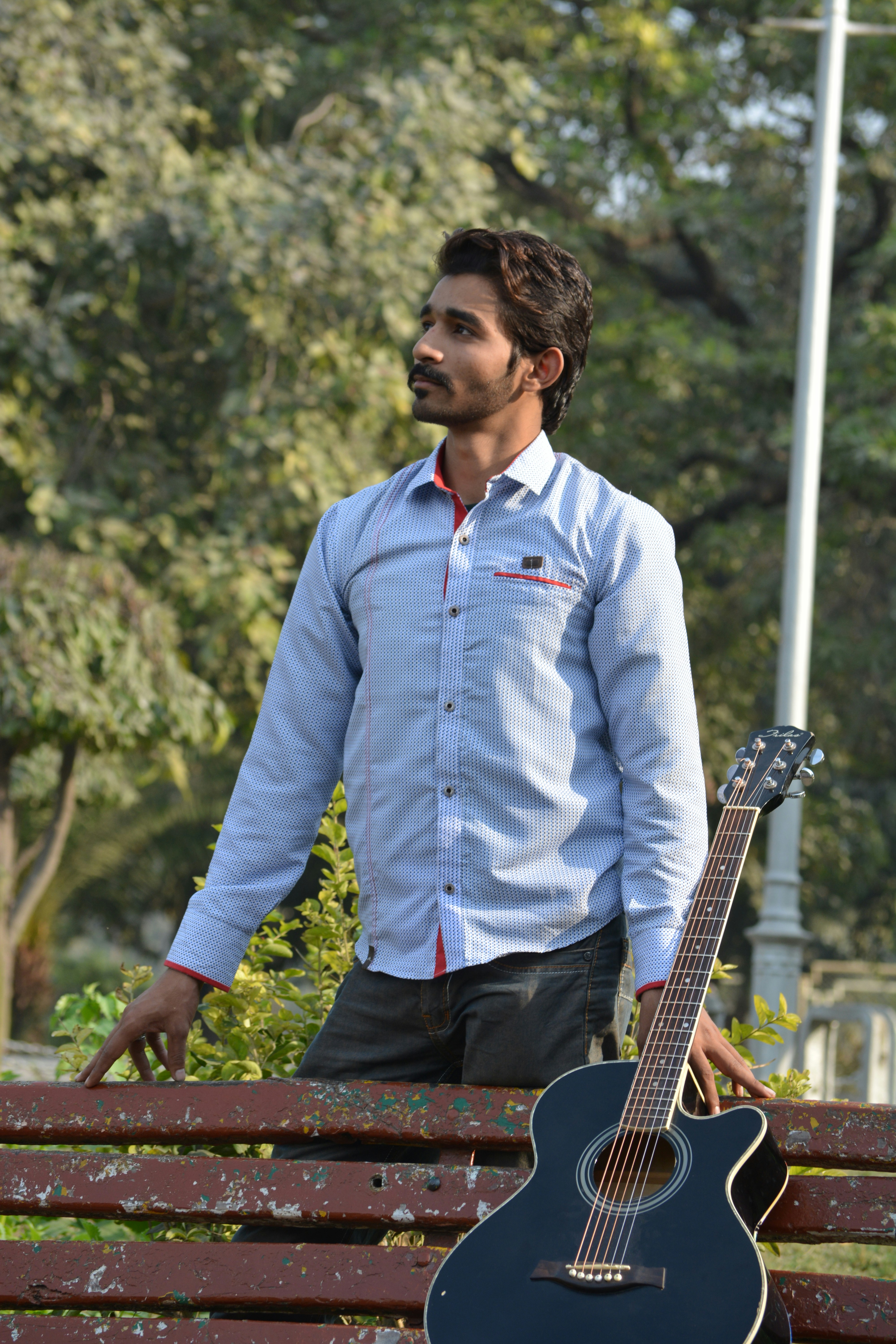 Parkside Serenade: Portrait of a guitarist pausing beside a weathered park bench