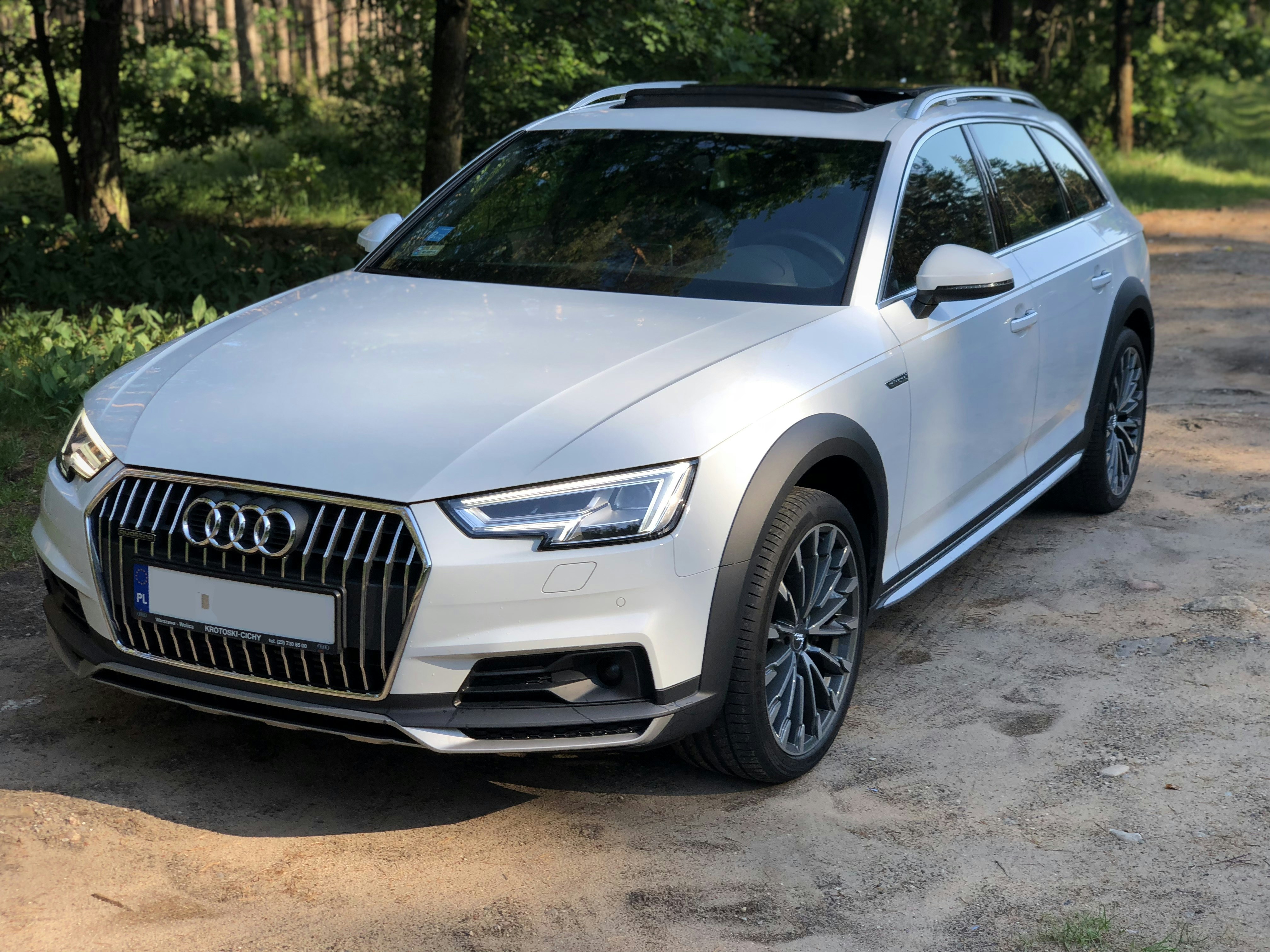 Audi A4 Allroad parked on a sandy path surrounded by lush greenery, showcasing its sleek design and rugged capabilities.