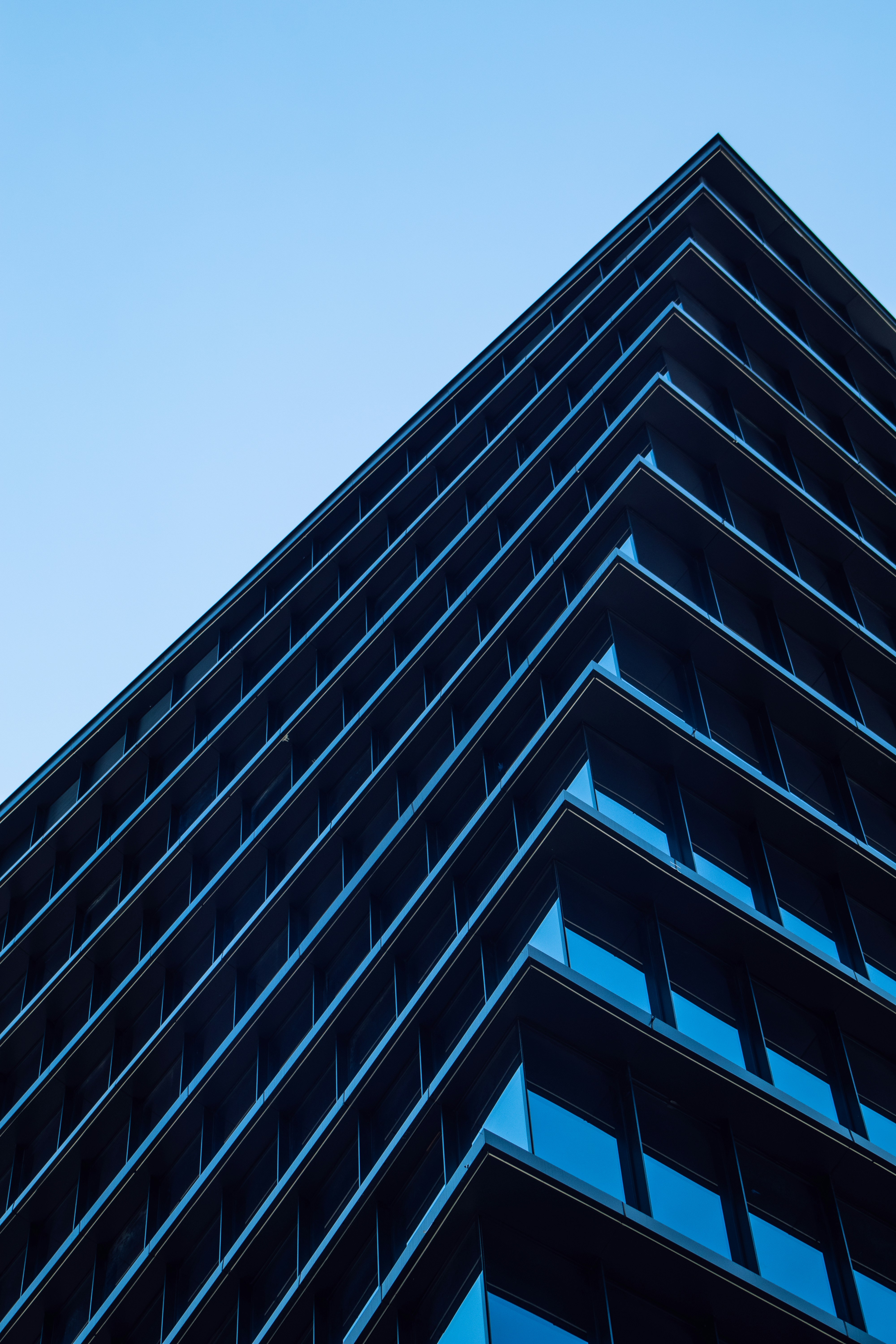 Angular view of a contemporary building, showcasing its sleek glass facade and geometric lines against a clear blue sky.