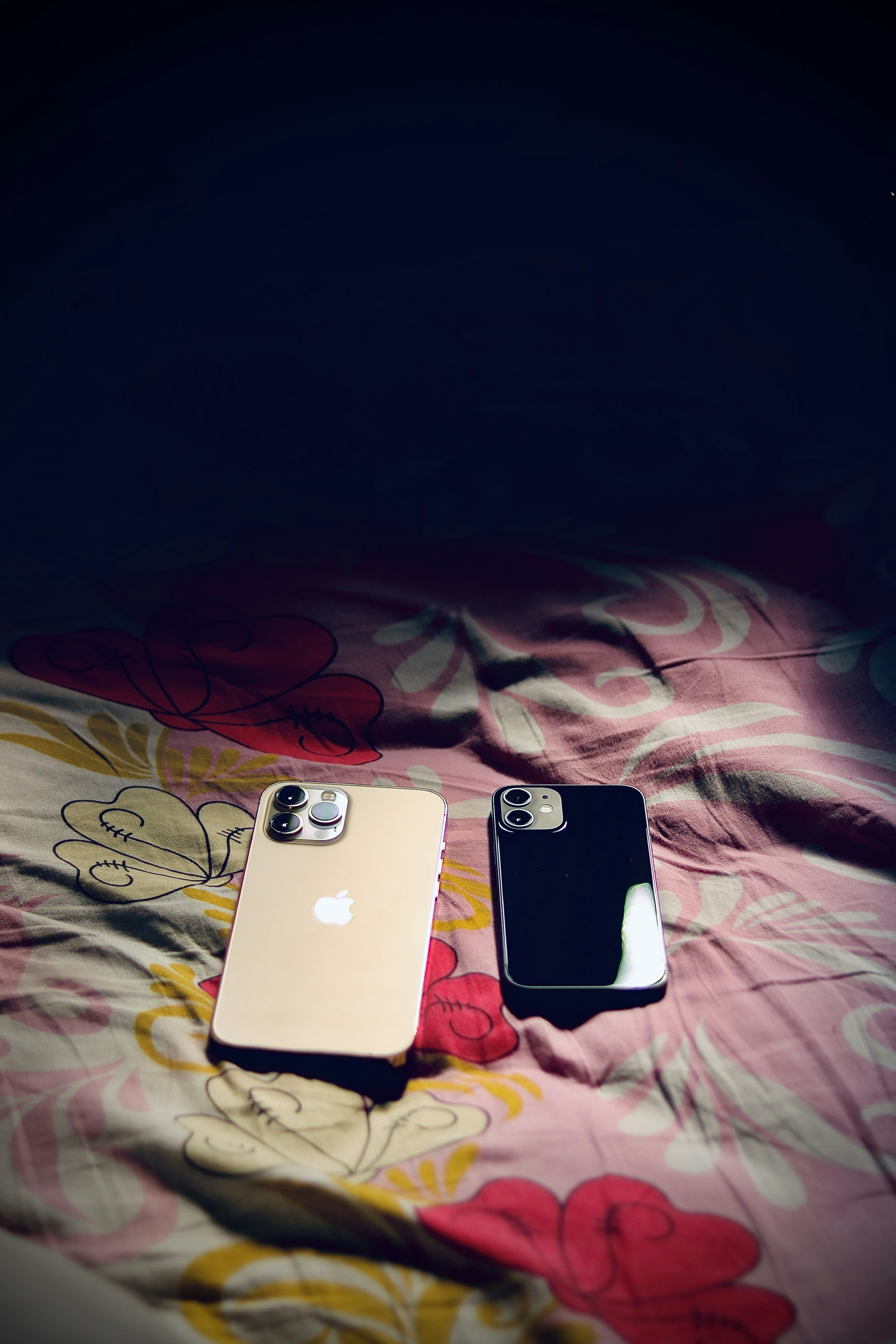 Gold and Shadow: Two iPhones Rest on a Floral Bedspread