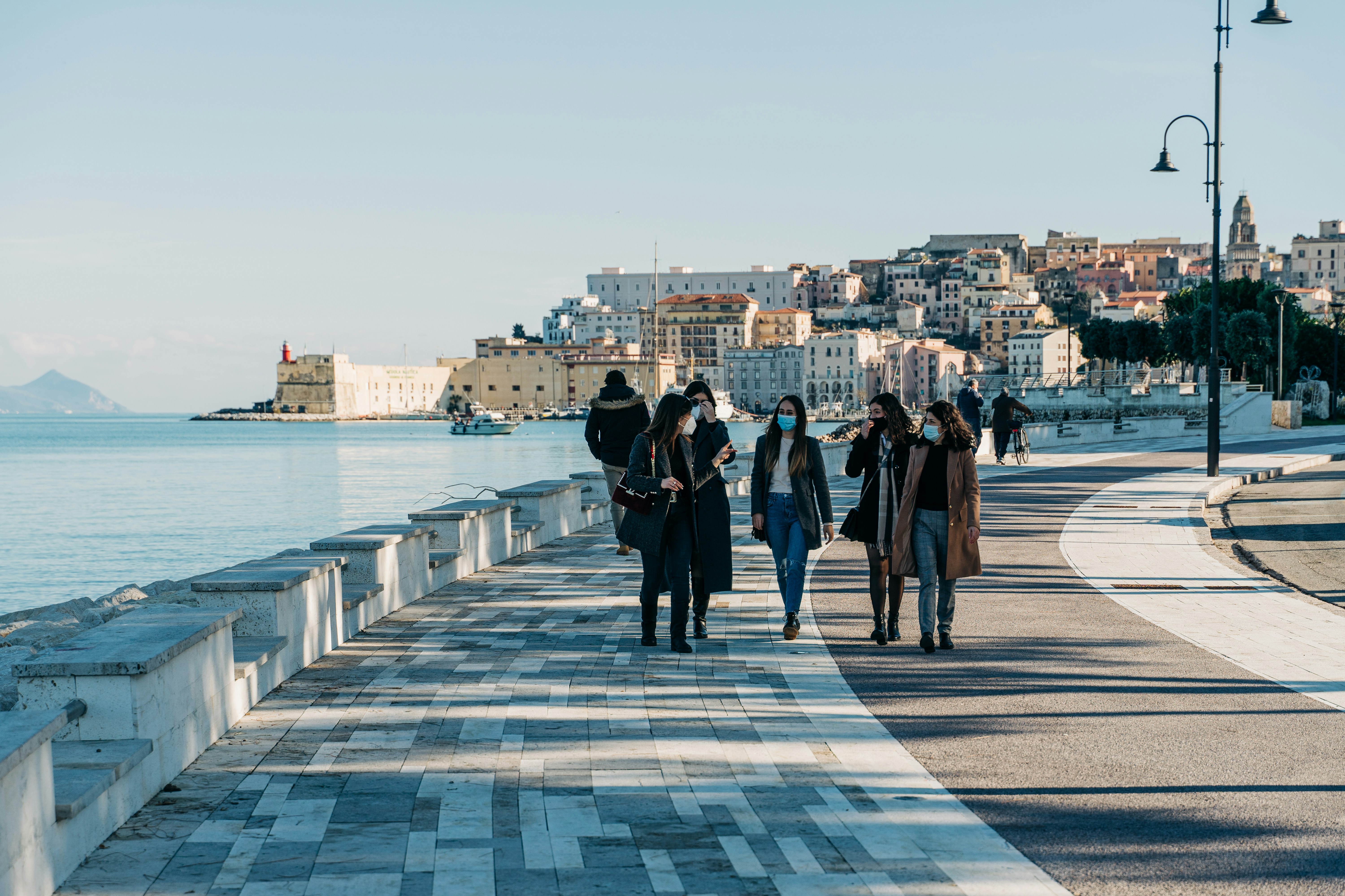 Girls in face masks chatting and walking along the waterfront in Gaeta, Italy