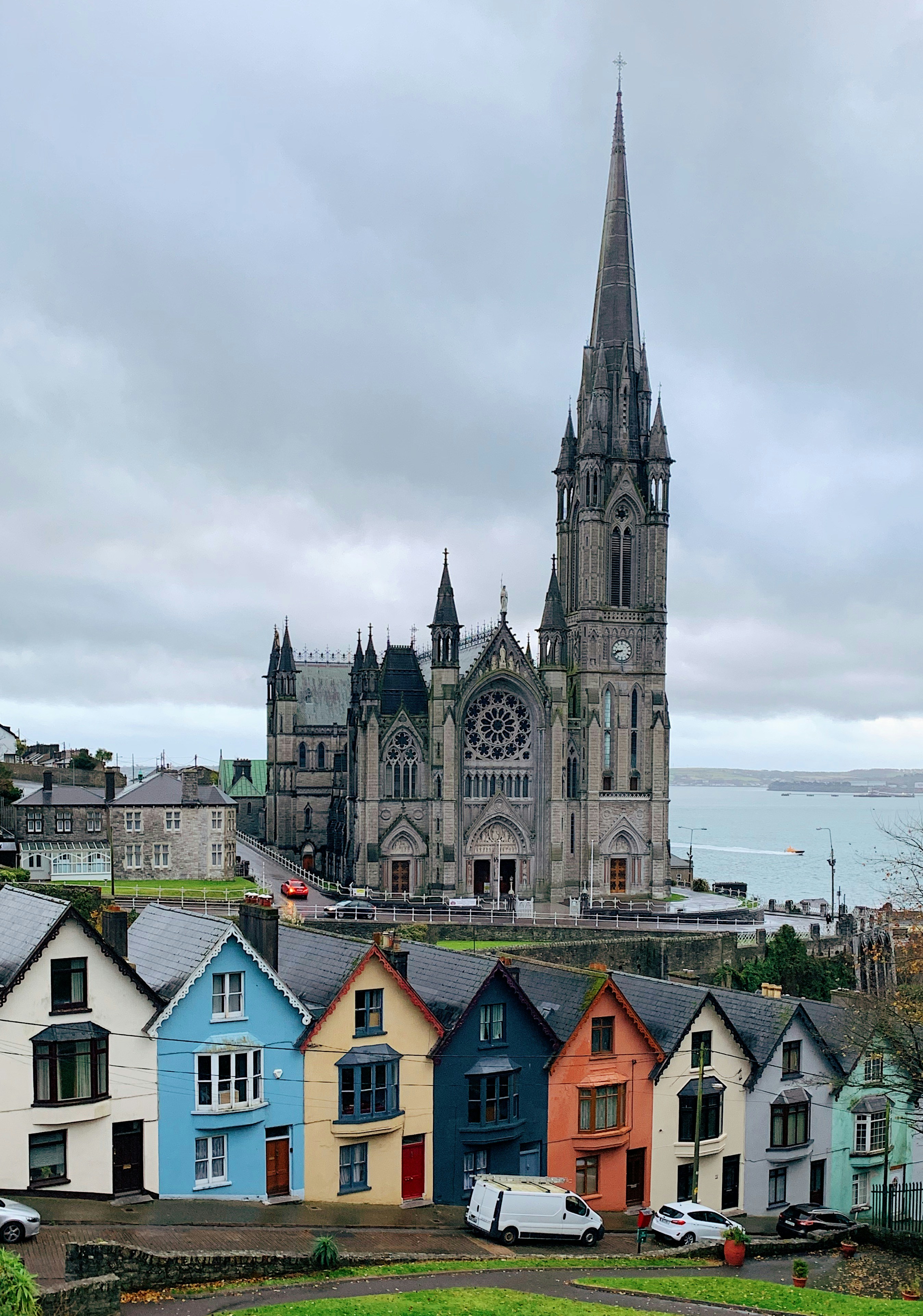 Gothic cathedral towers over a row of vibrantly painted houses, showcasing a blend of architectural styles. A serene harbor can be seen in the background.