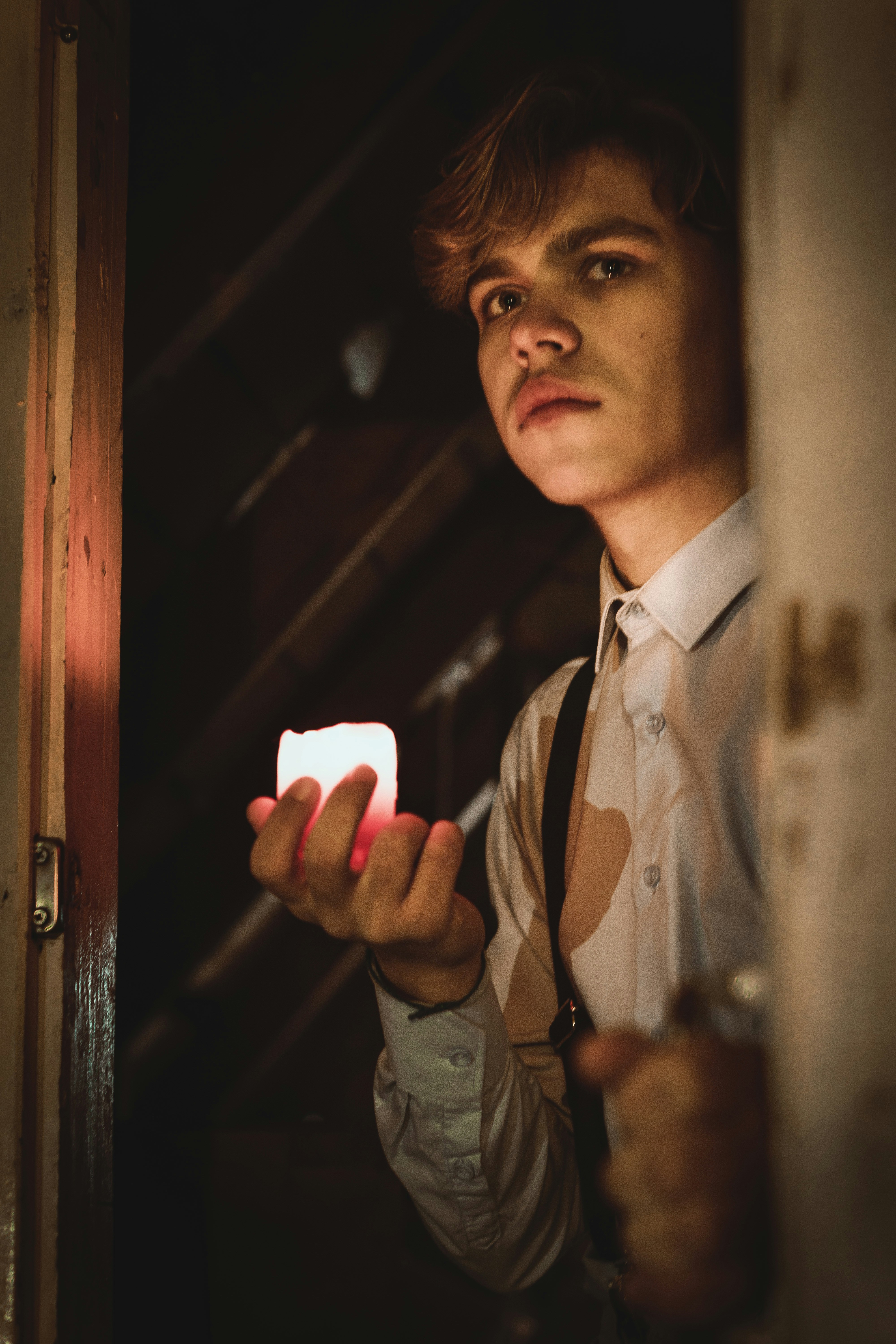 Young man holding a glowing candle while peering through a doorway, creating an atmosphere of mystery and intrigue.