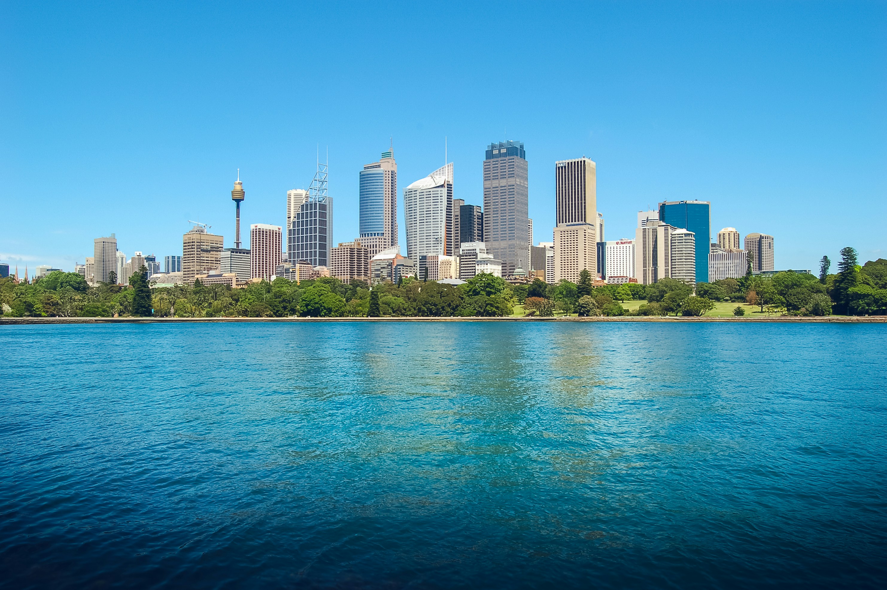 Sydney skyline reflected in the calm waters under a clear blue sky.