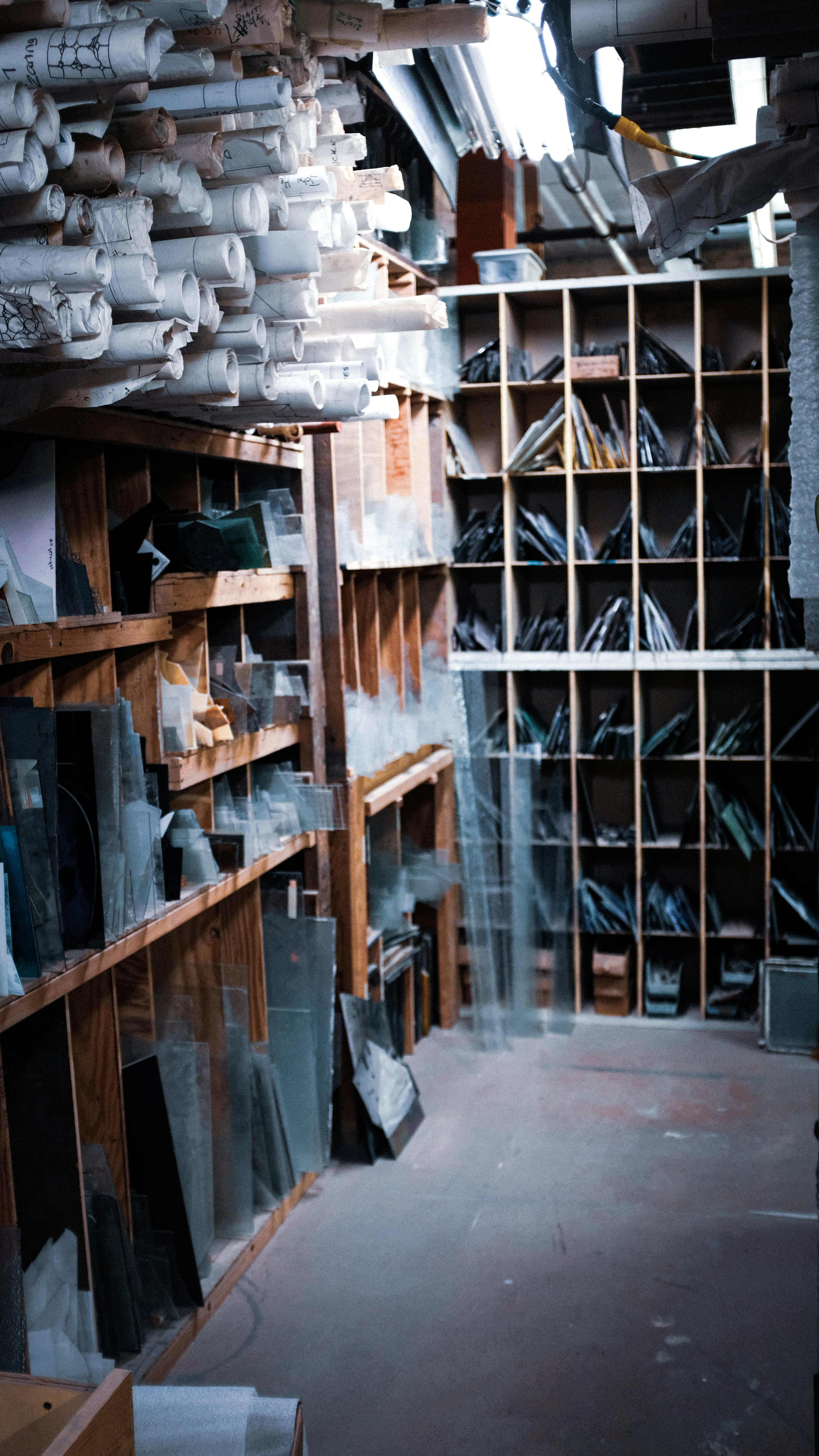 An organized storage area filled with various sheets of glass and rolls of paper, showcasing the blend of materials in a workshop setting.