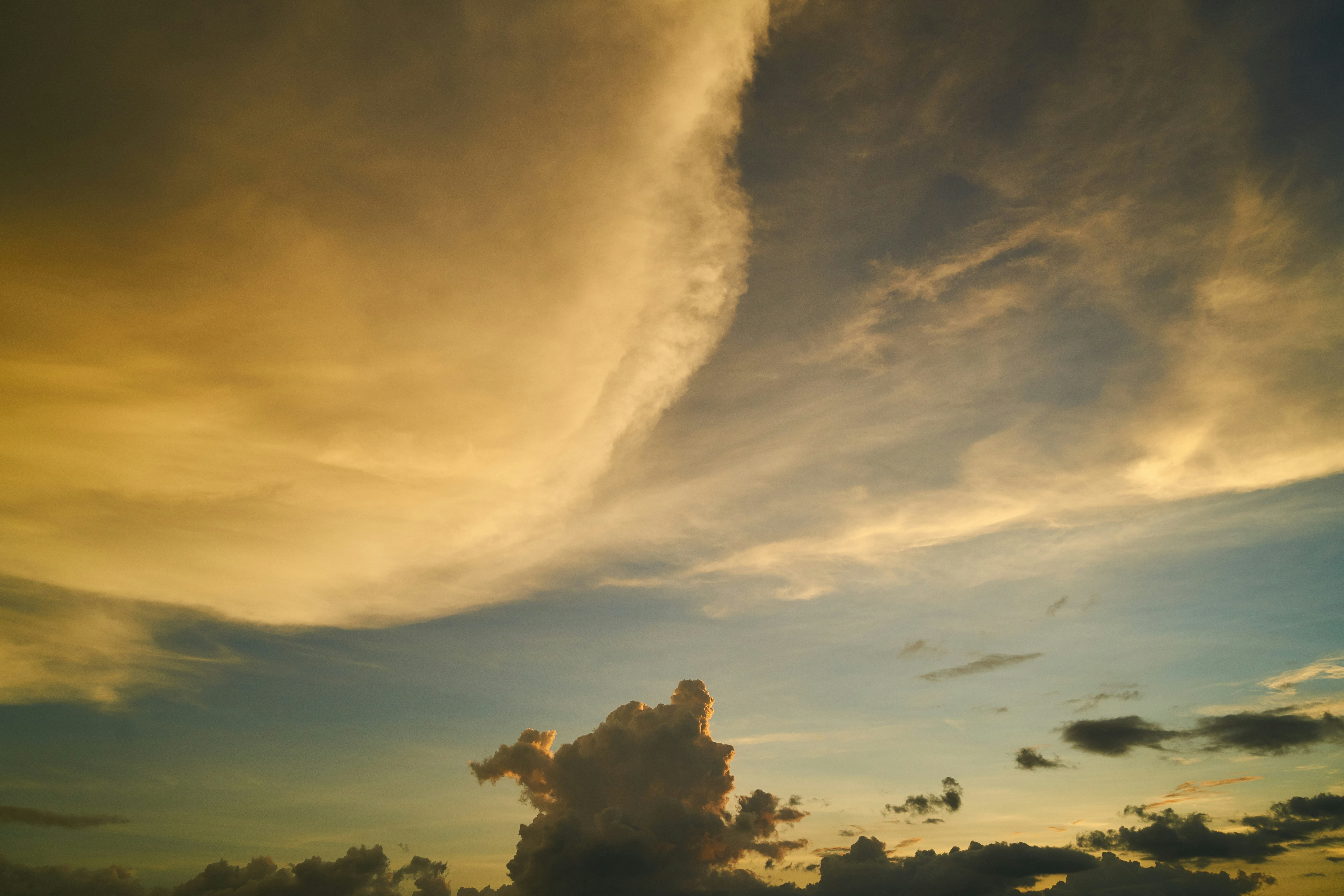Dramatic clouds illuminated by golden hues transition into twilight, creating a serene atmosphere. The scene captures the beauty of the sky at dusk.