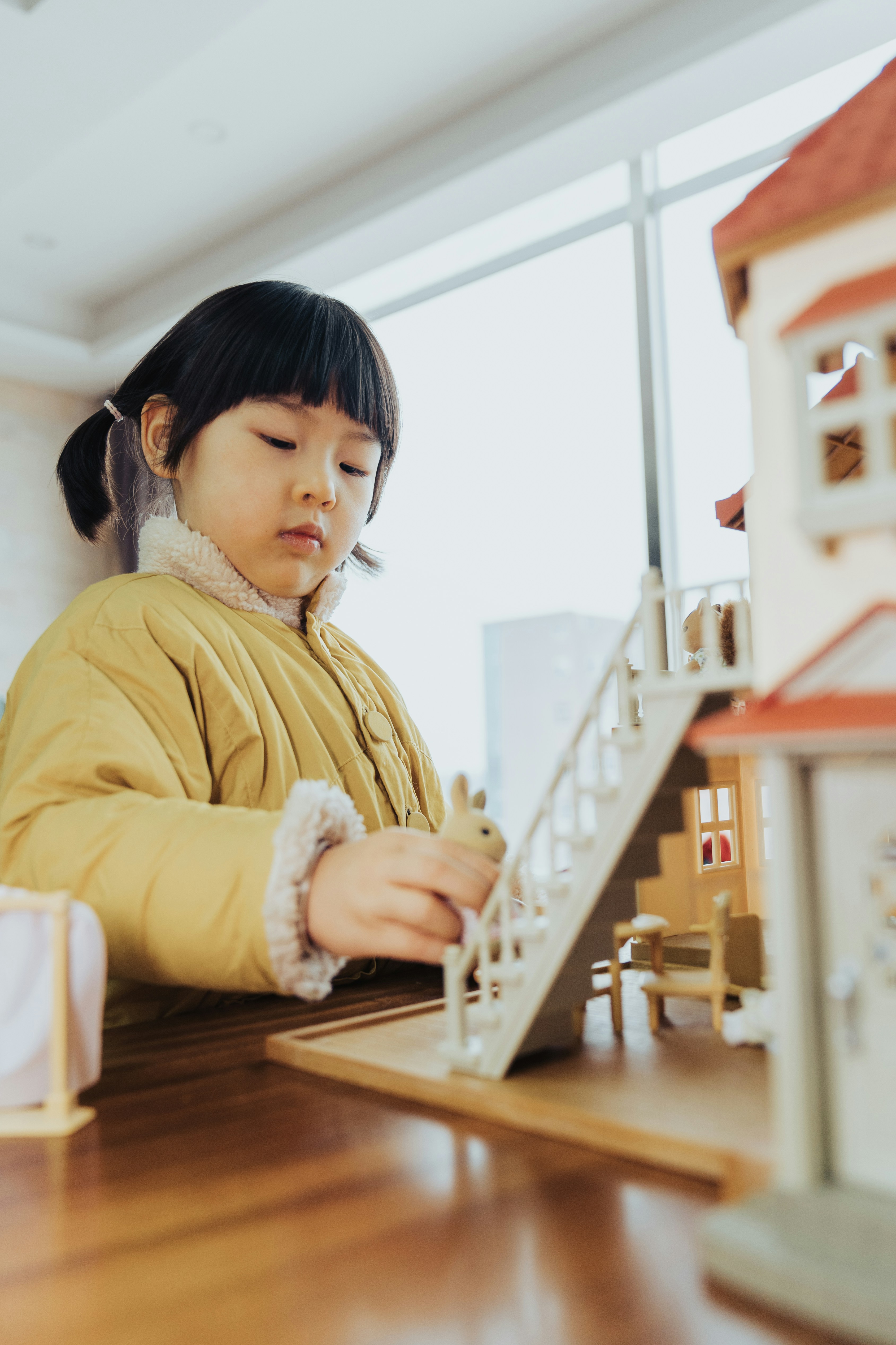 Child engrossed in play with a miniature house and figurines, showcasing creativity and joy. The scene captures a moment of childhood wonder.