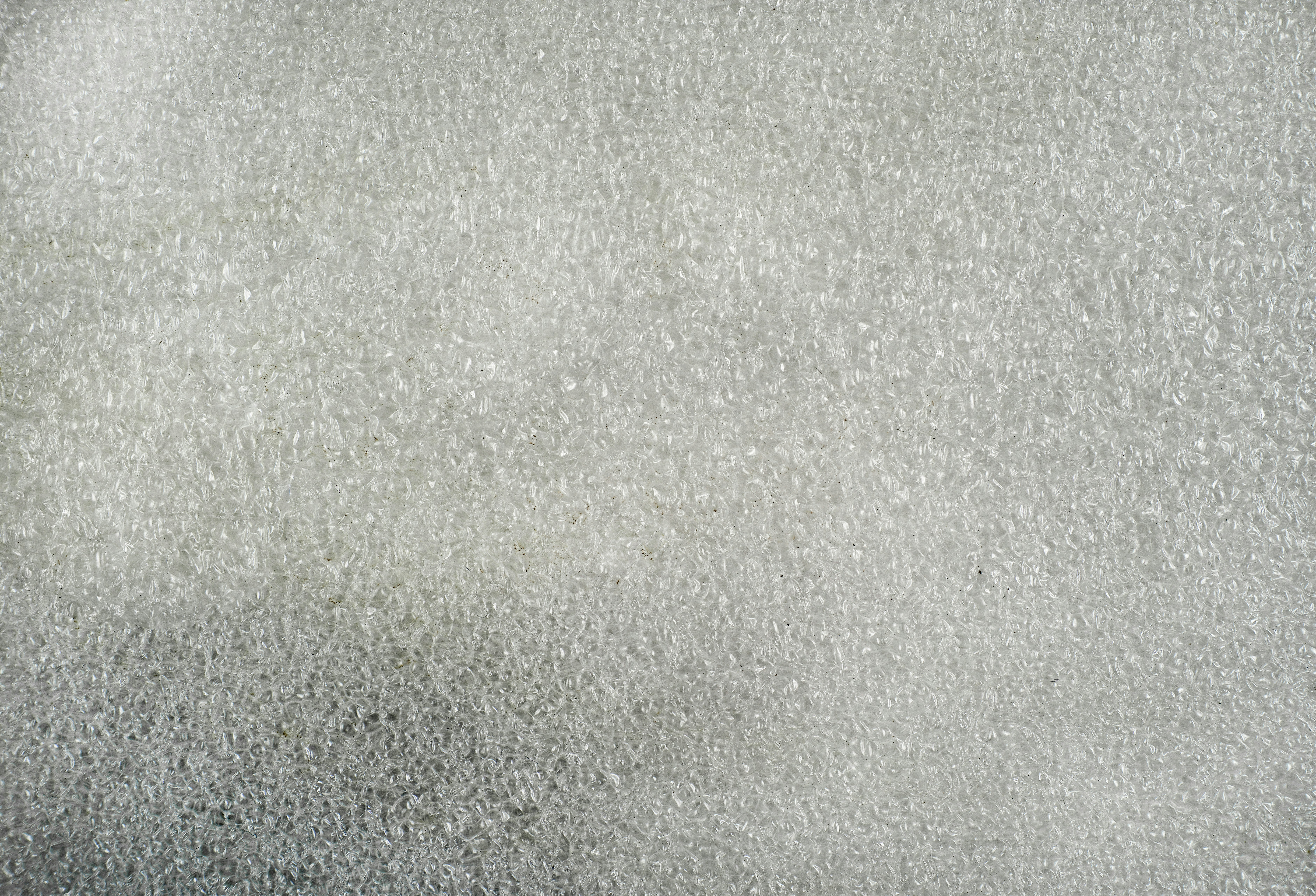 Close-up of a textured surface exhibiting a myriad of tiny bubbles and reflections. The intricate details create a unique visual rhythm.