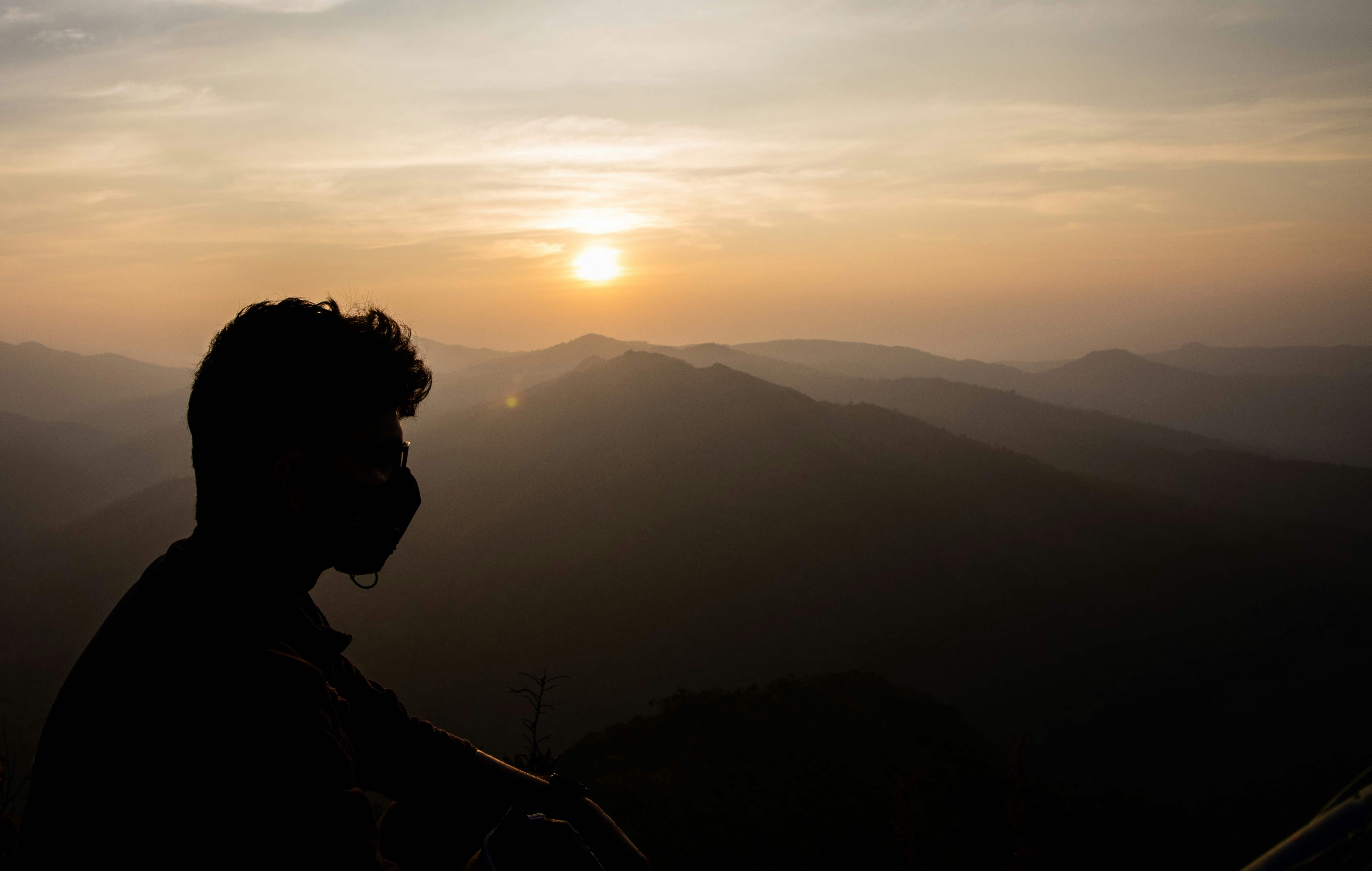 Silhouette of a person wearing a mask against a backdrop of rolling hills at sunset.