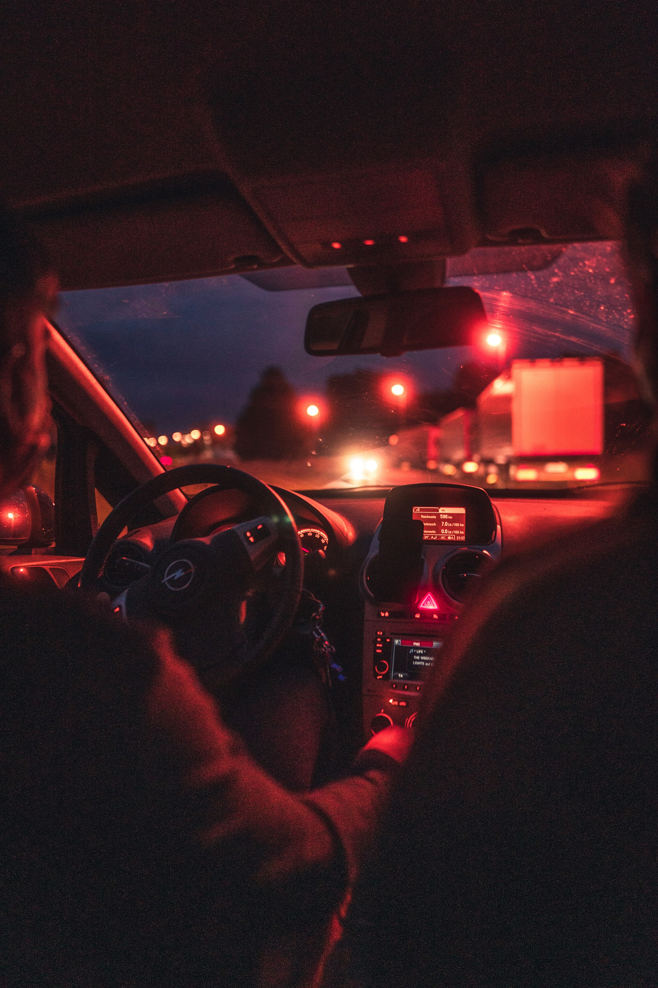 Interior view of a car with a focus on the dashboard illuminated in red, capturing the ambiance of a nighttime drive amidst city lights.