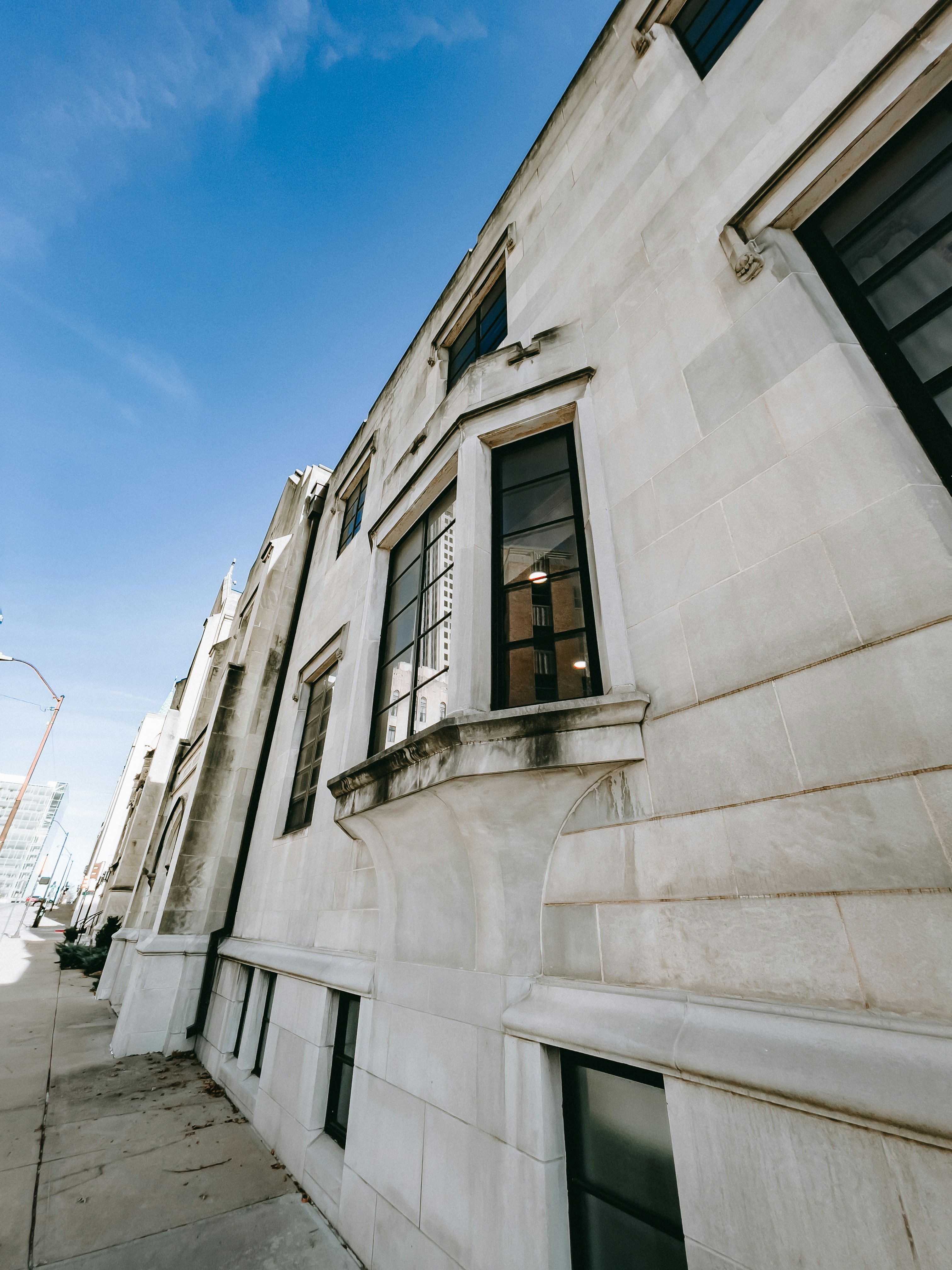 Low-angle view of a white stone building with large windows against a clear blue sky.