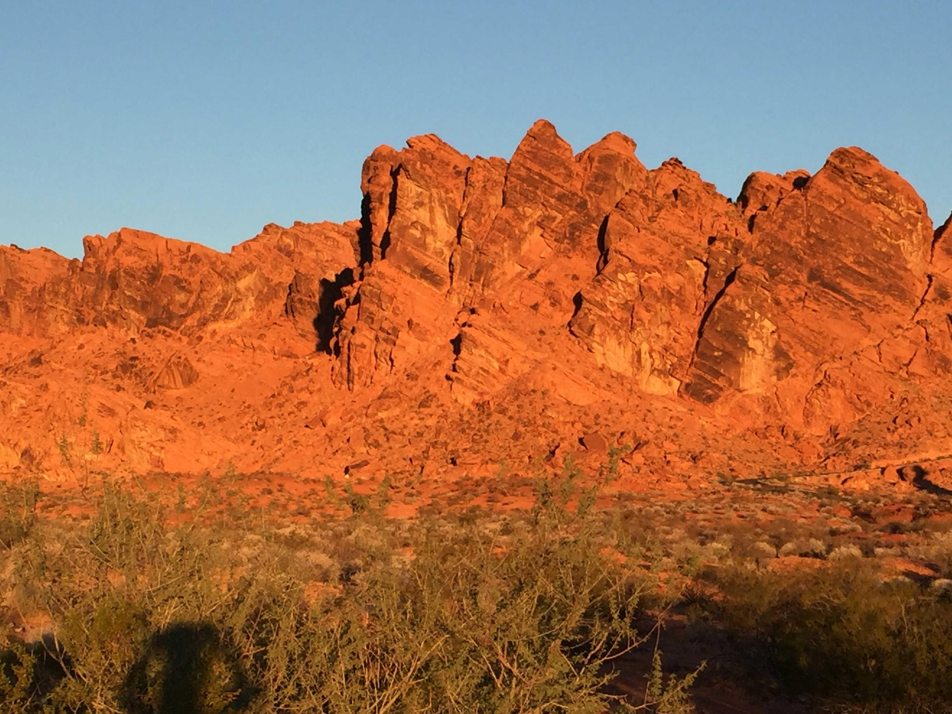 Rugged orange cliffs illuminated by warm sunset light against a clear blue sky.