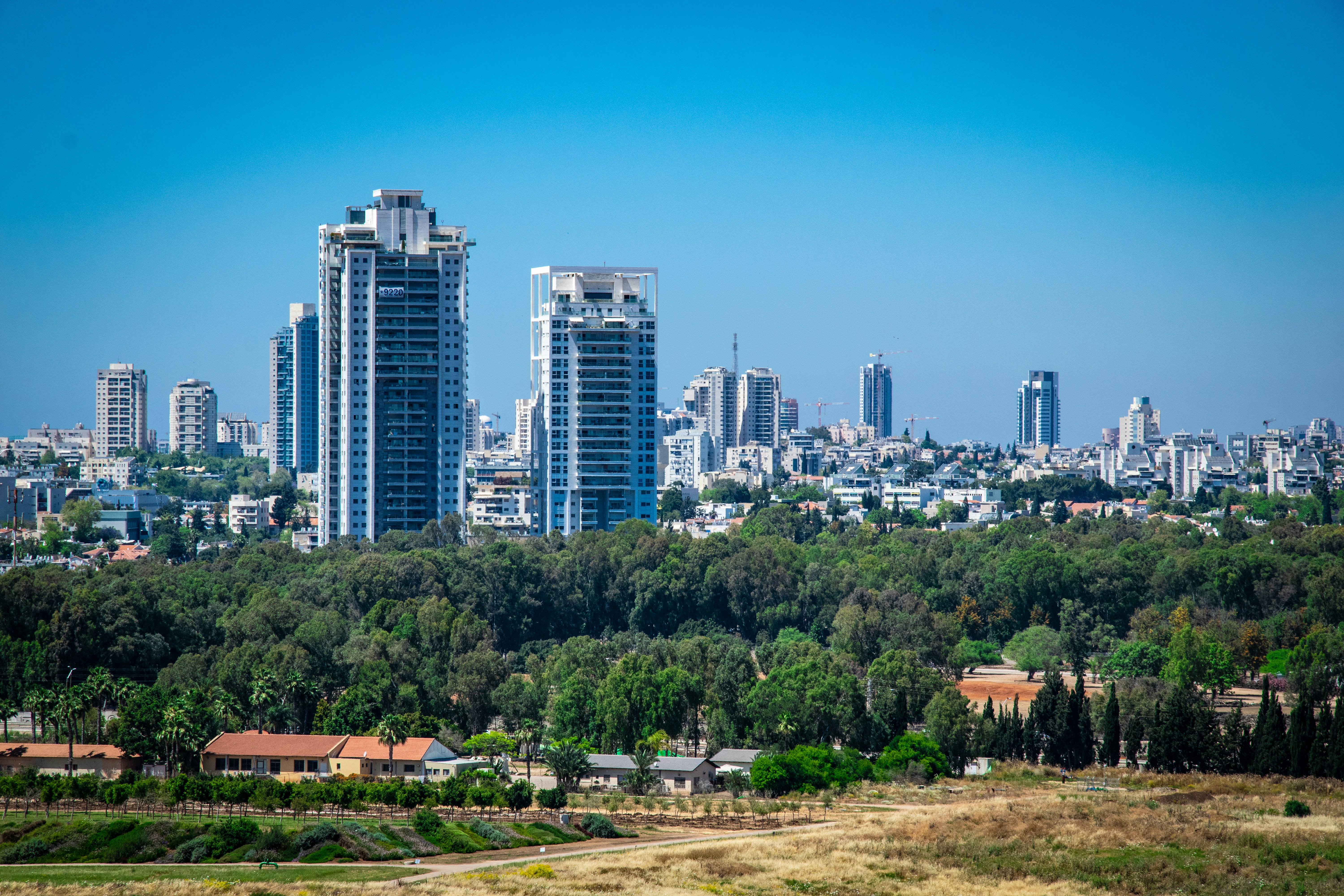 City skyline featuring contemporary high-rise buildings set against a backdrop of lush greenery and residential areas.