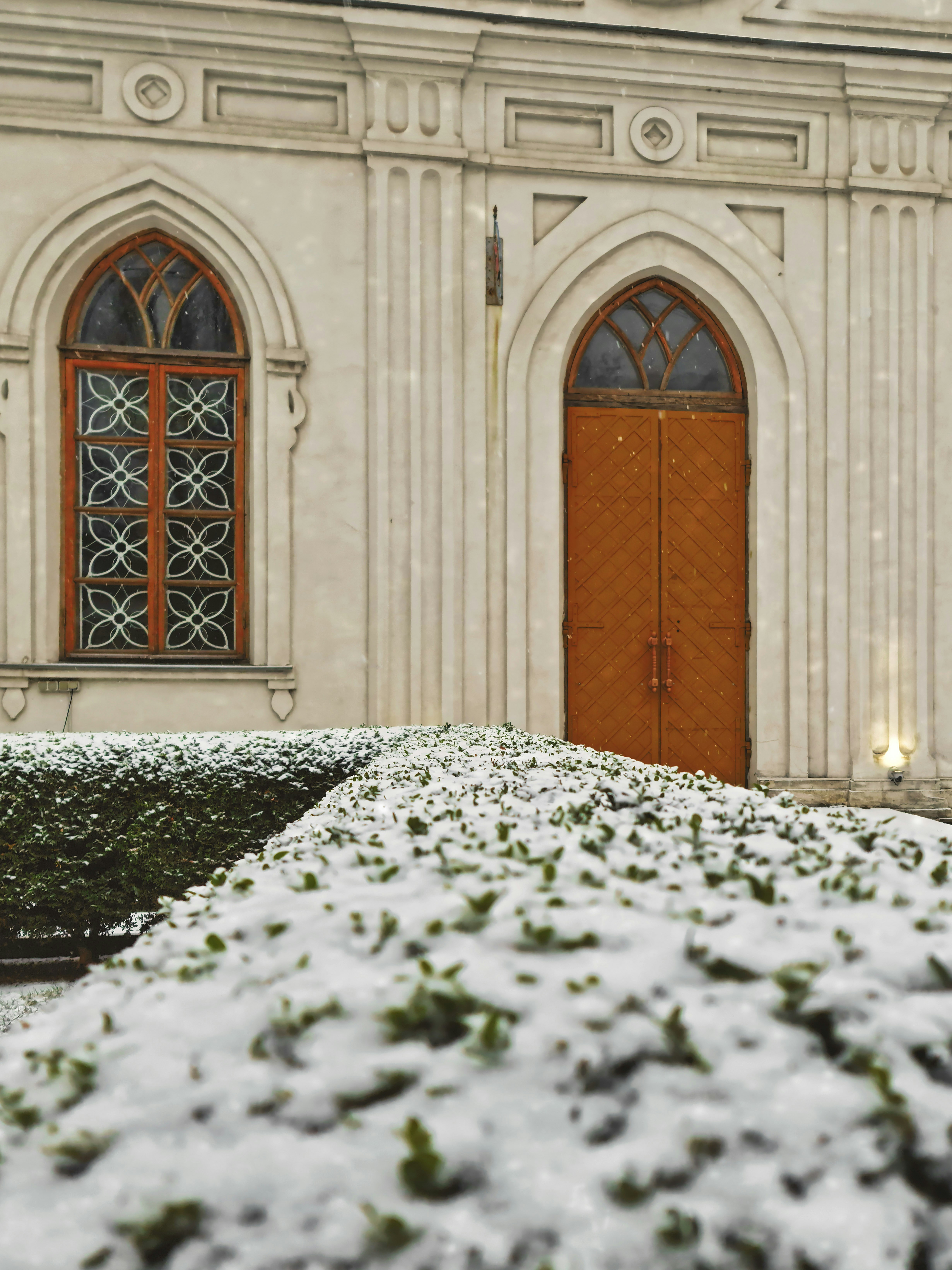 Snow-Dusted Facade: Arched Windows and a Wooden Door Framed by Winter Hedge
