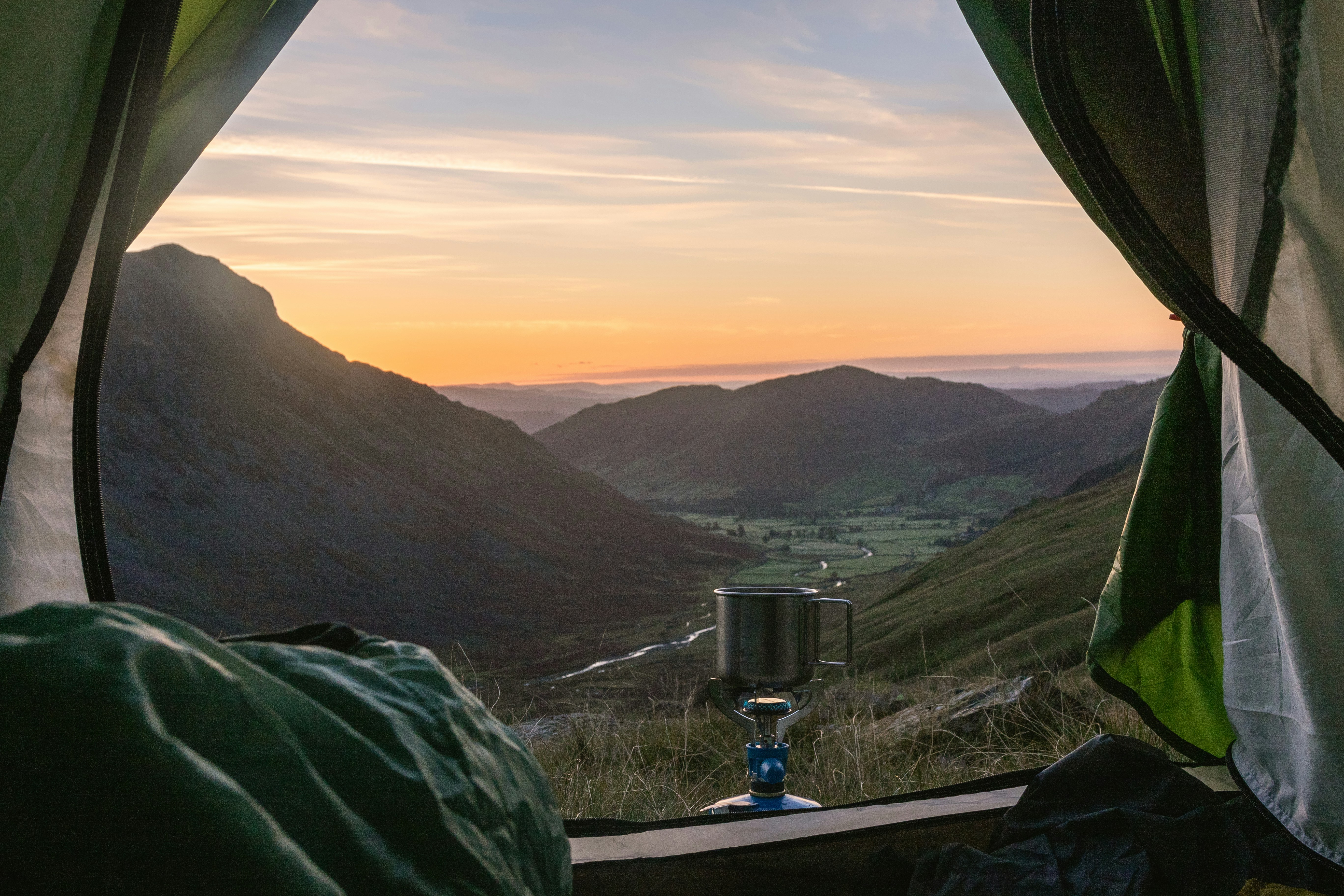 Dawn Over the Valley: Tent Window View with a Compact Stove in the Foreground