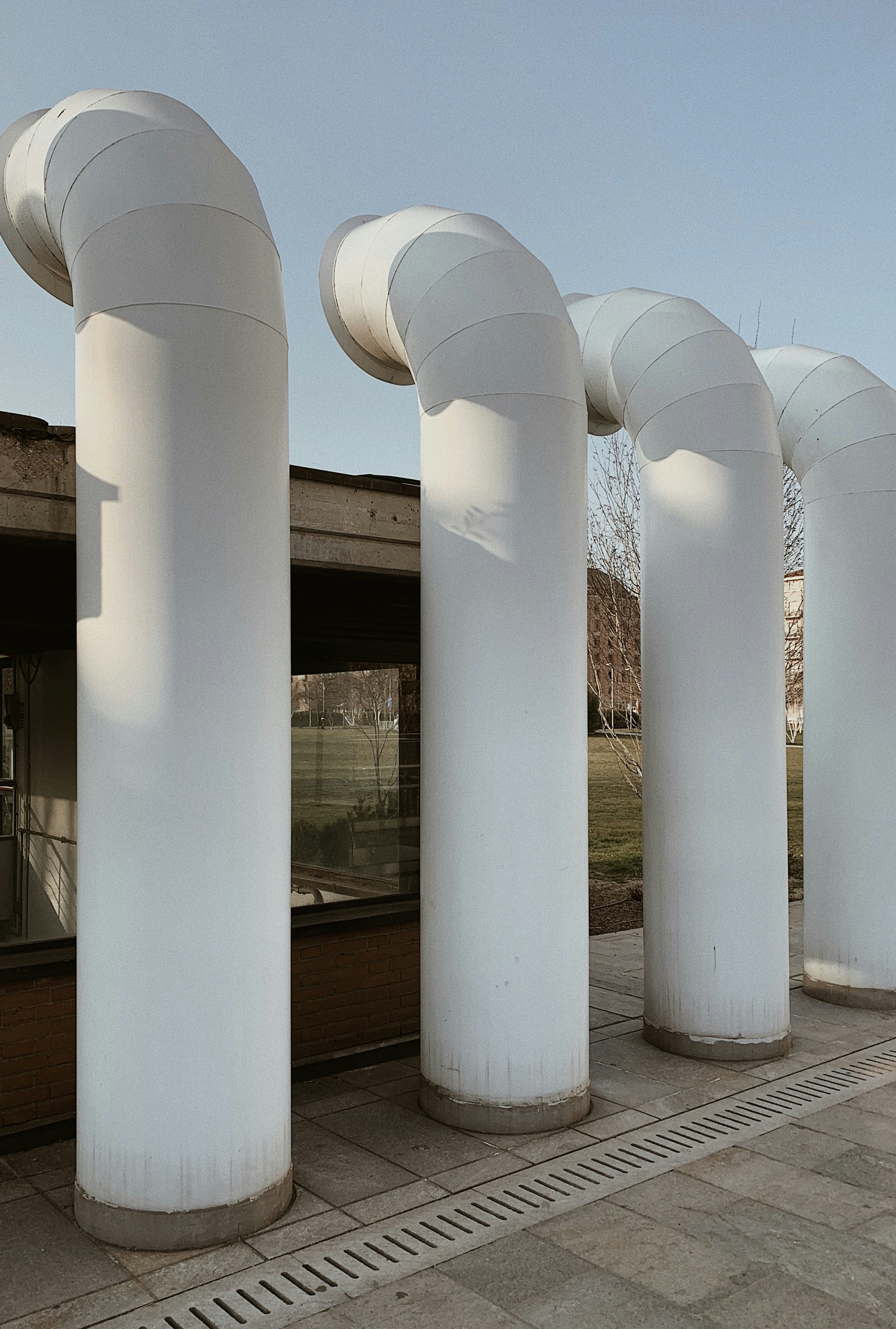 Sunlit Arcs: Three White Pipes Stretch Across a Quiet Campus