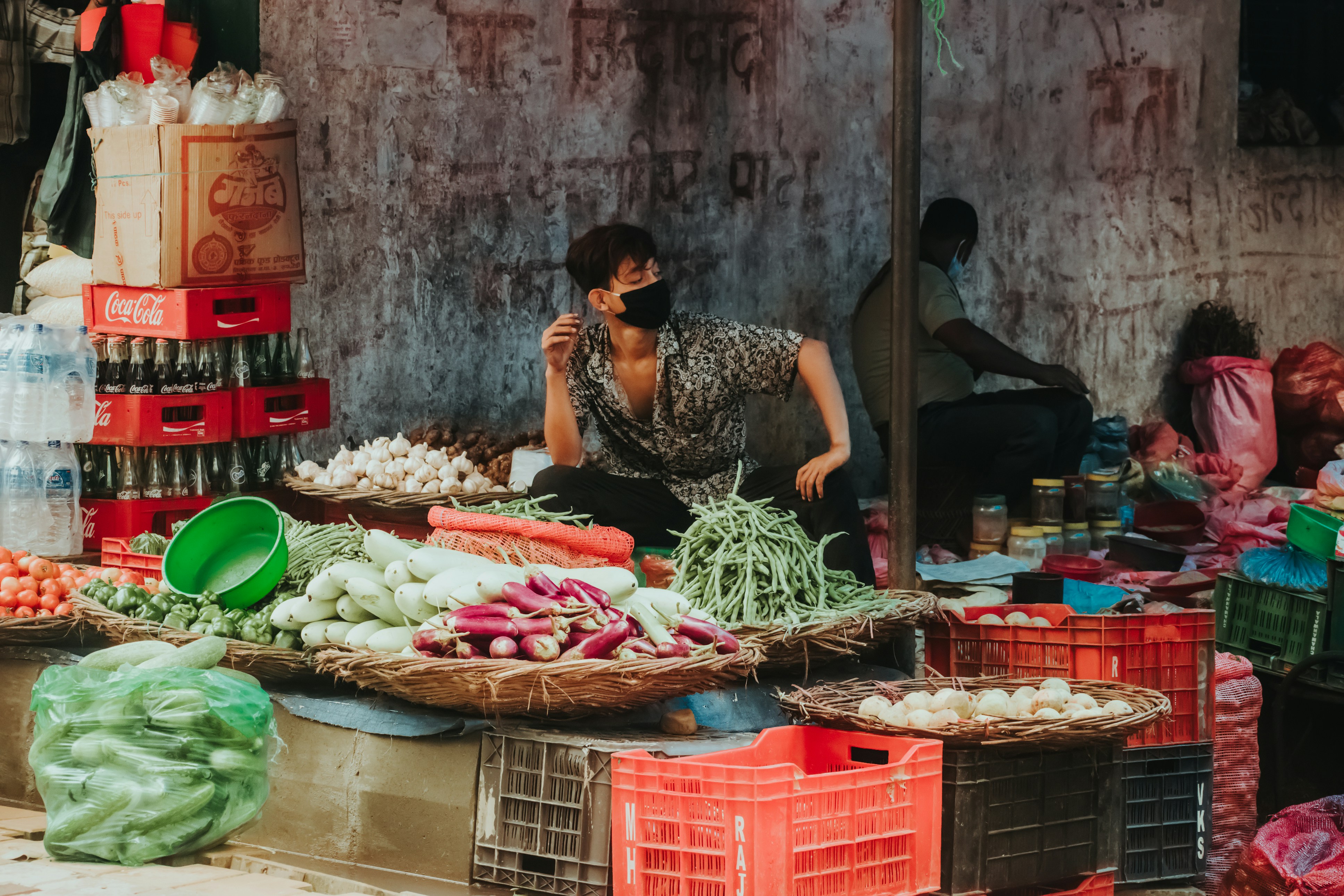A bustling market scene featuring a vendor surrounded by vibrant vegetables and goods, conveying the essence of local commerce and community interaction.