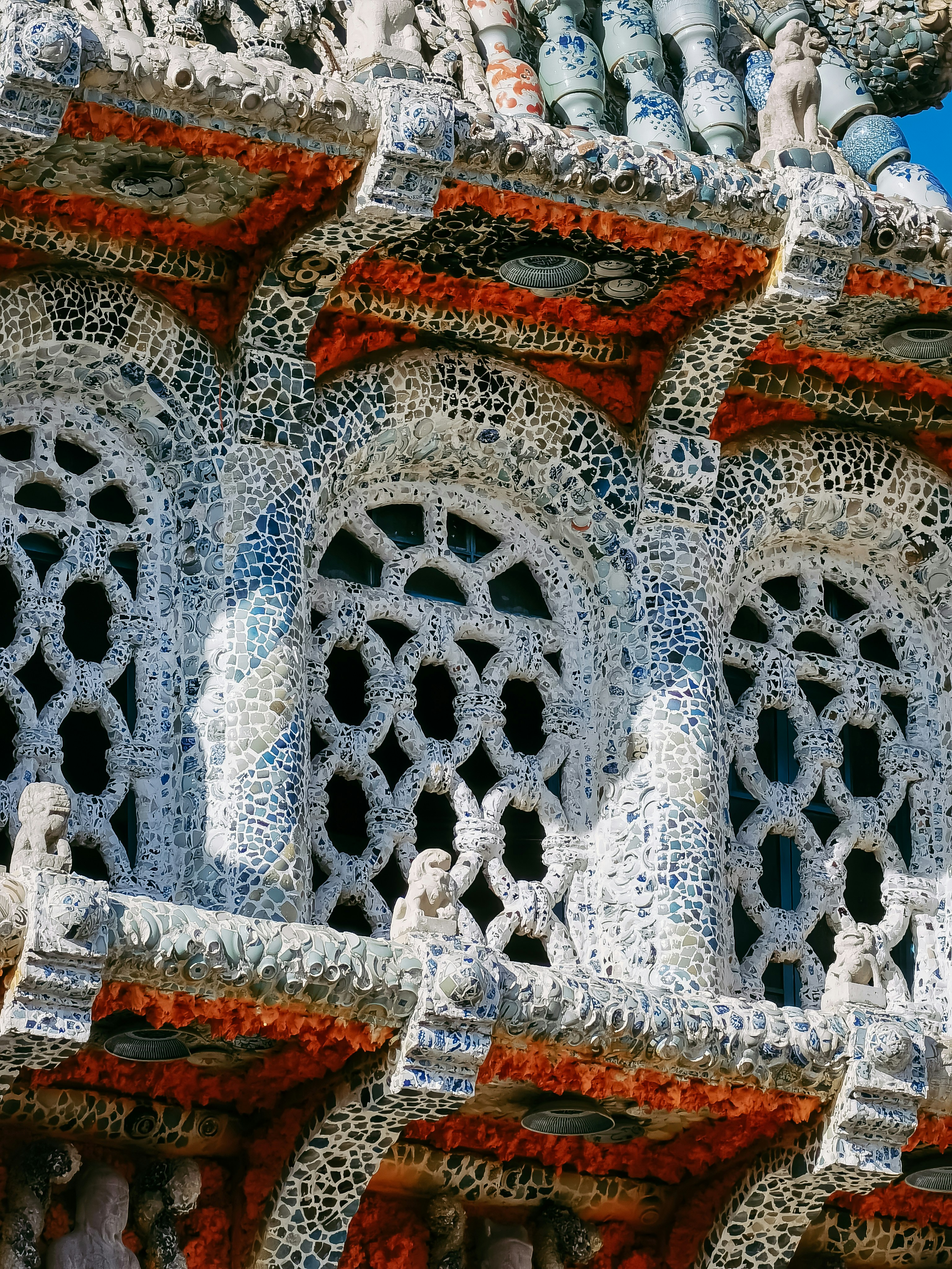 Close-up of a mosaic facade with blue-and-white tessellation and red accents. Ornate lattice arches and carved details define the scene.