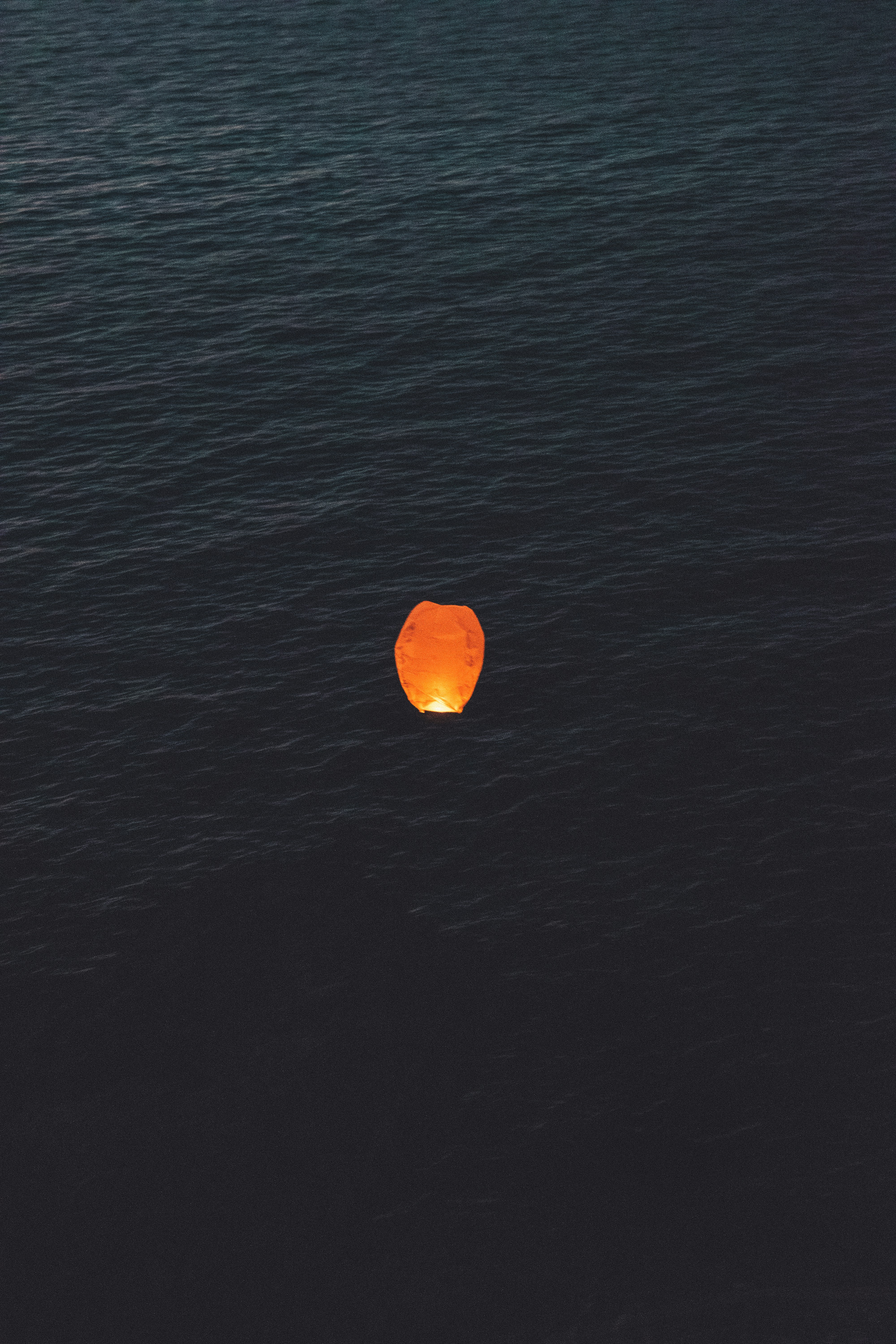 Floating Flame: An Orange Lantern Drifts Over Dark Seas