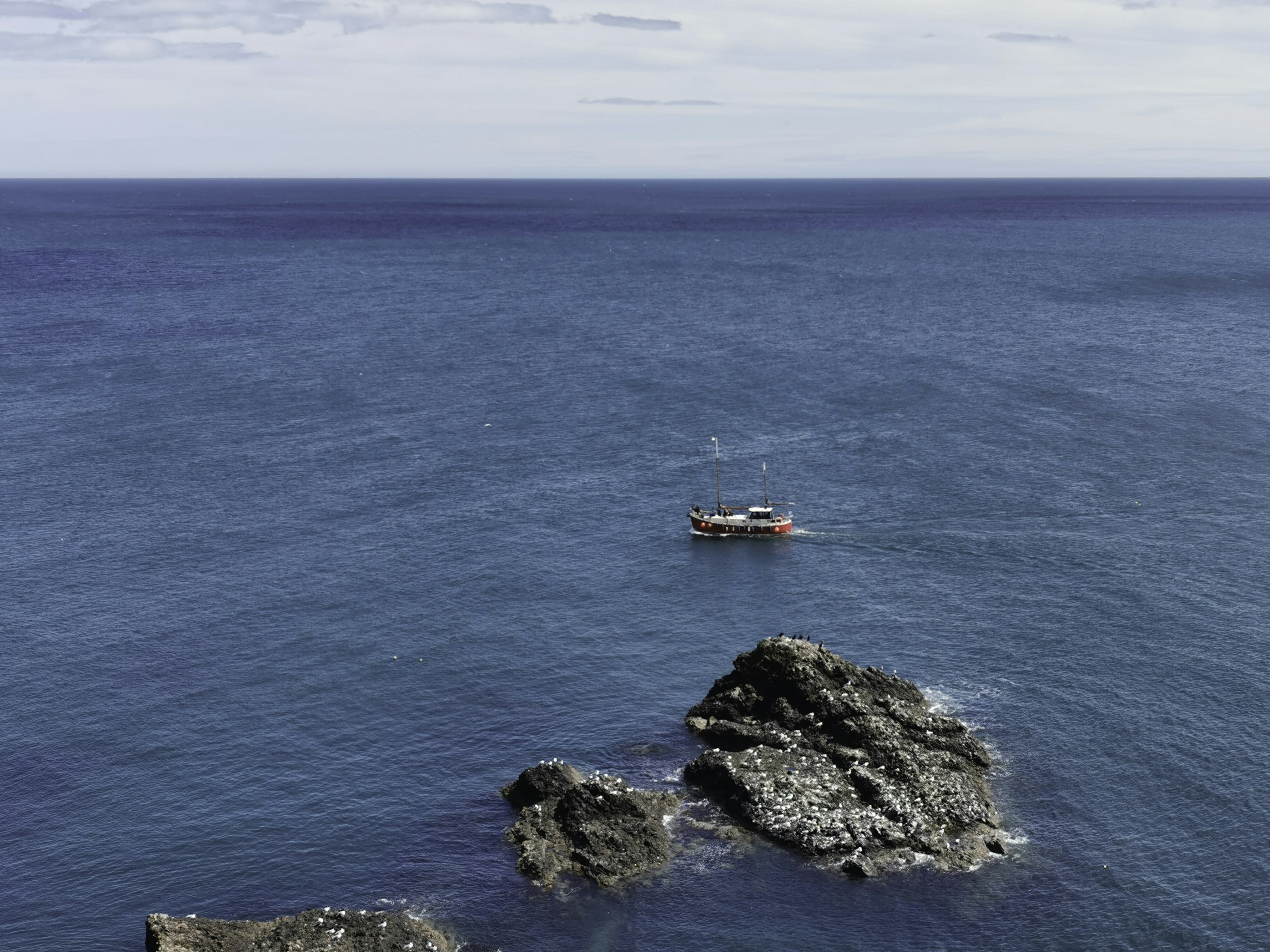 Small boat navigating the expansive blue ocean near rocky formations under a clear sky.
