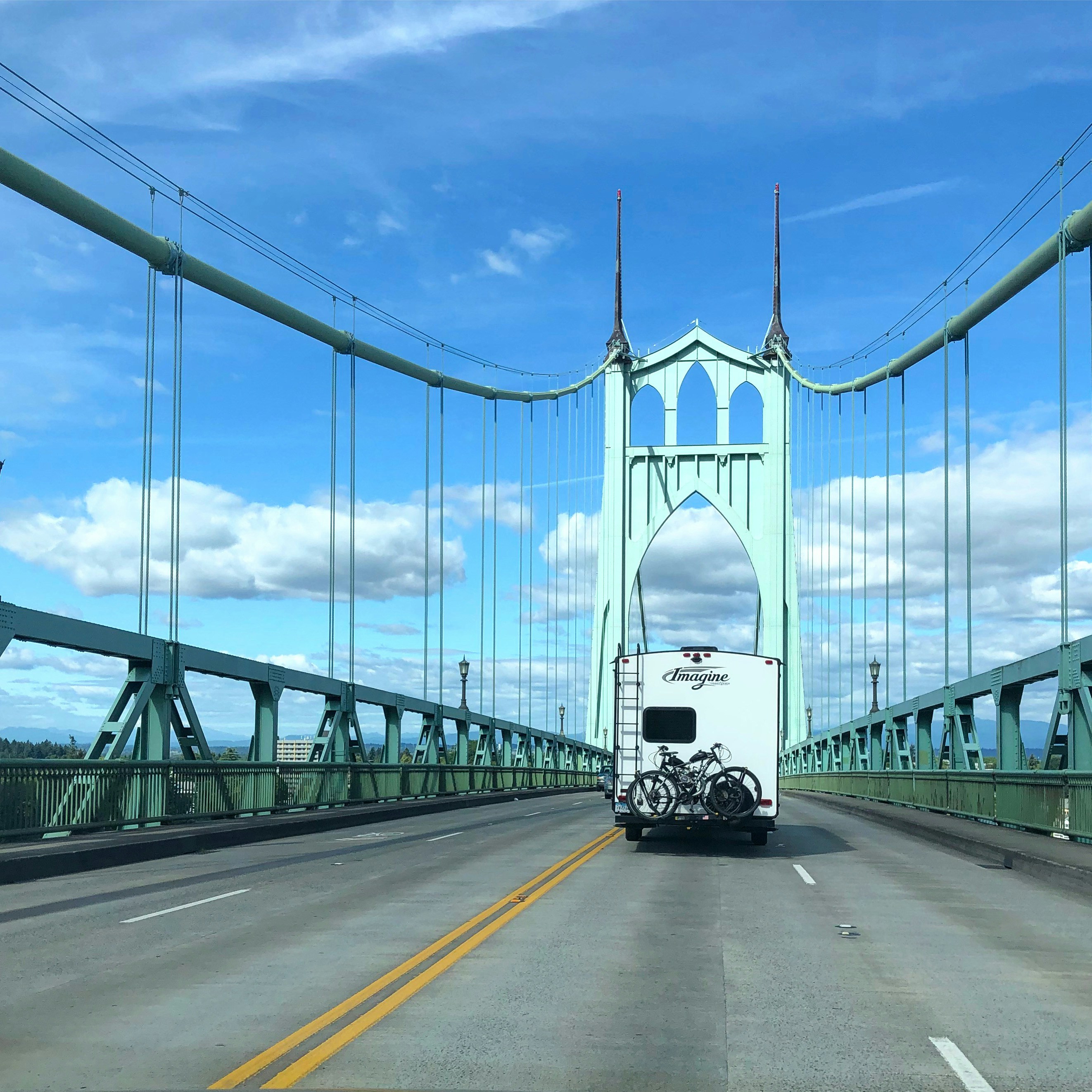 Bike-Racked Camper Crossing a Turquoise Suspension Bridge Under a Clear Sky