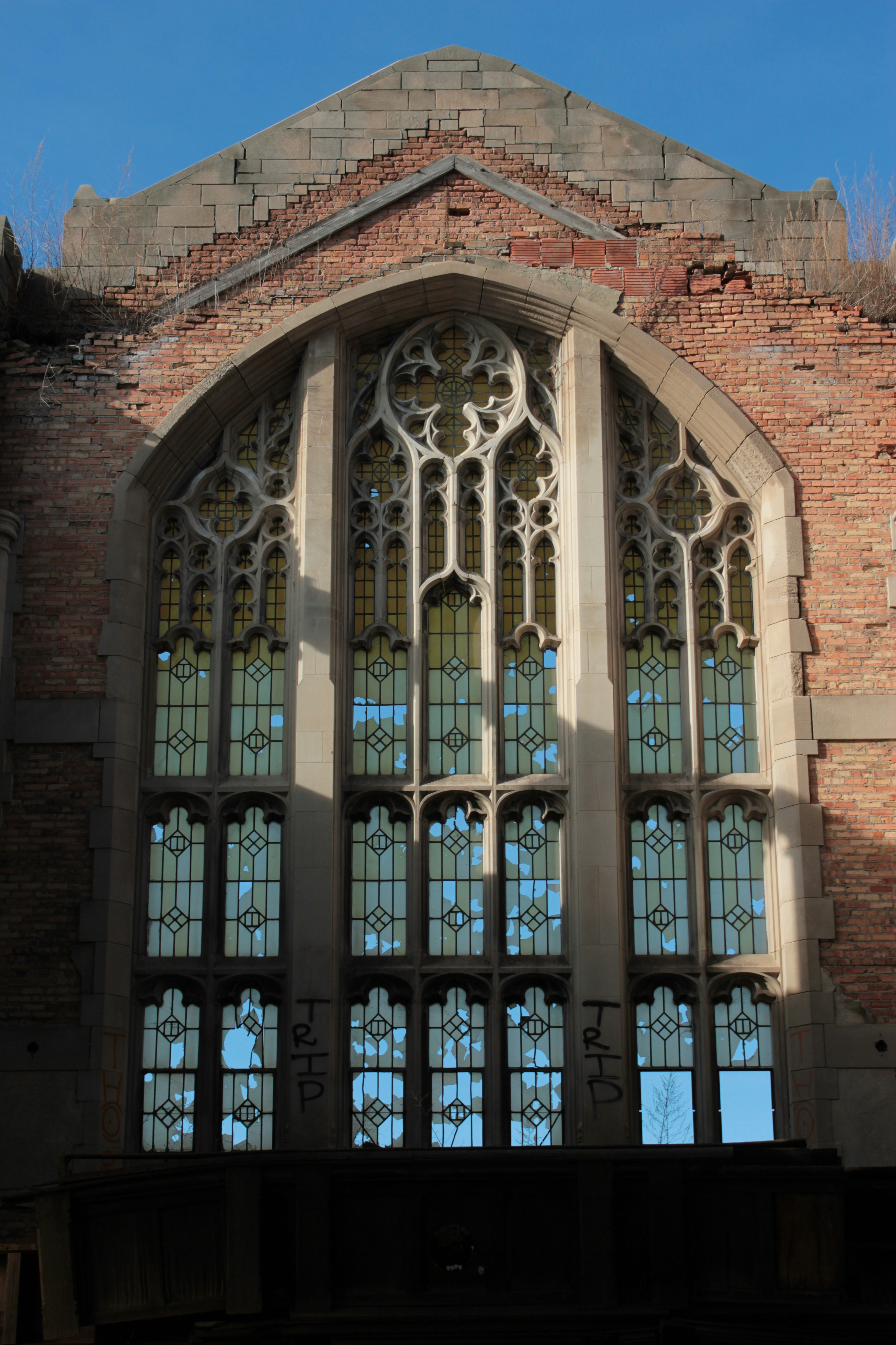 Intricate Gothic window with stained glass, framed by weathered brick walls, revealing the passage of time. Graffiti marks add a contemporary contrast.